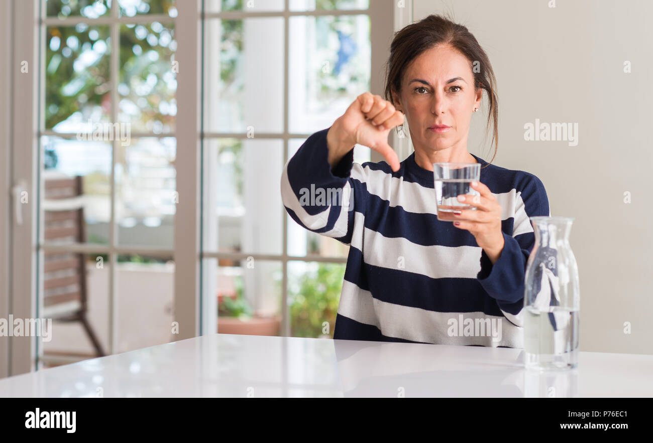 Middle aged woman drinking a glass of water with angry face, negative ...