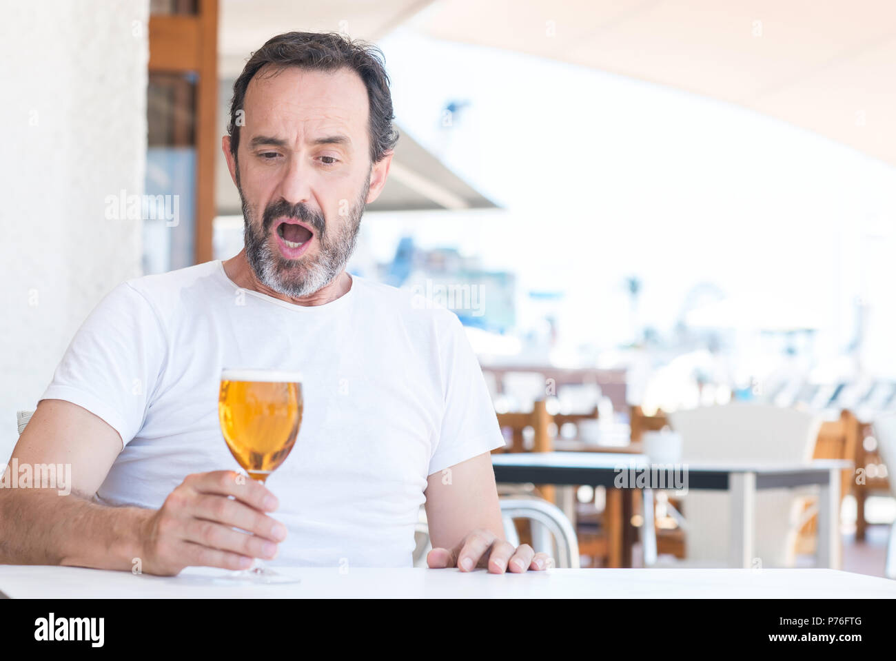 Handsome senior man drinking beer at restaurant scared in shock with a ...