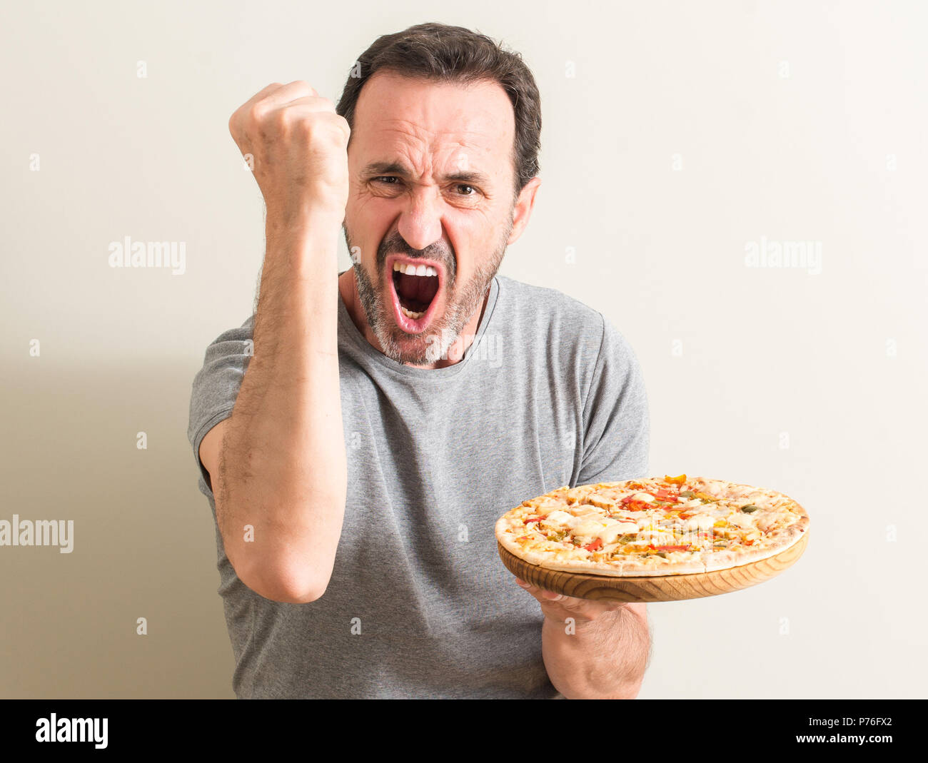 Senior man holding pizza annoyed and frustrated shouting with anger ...