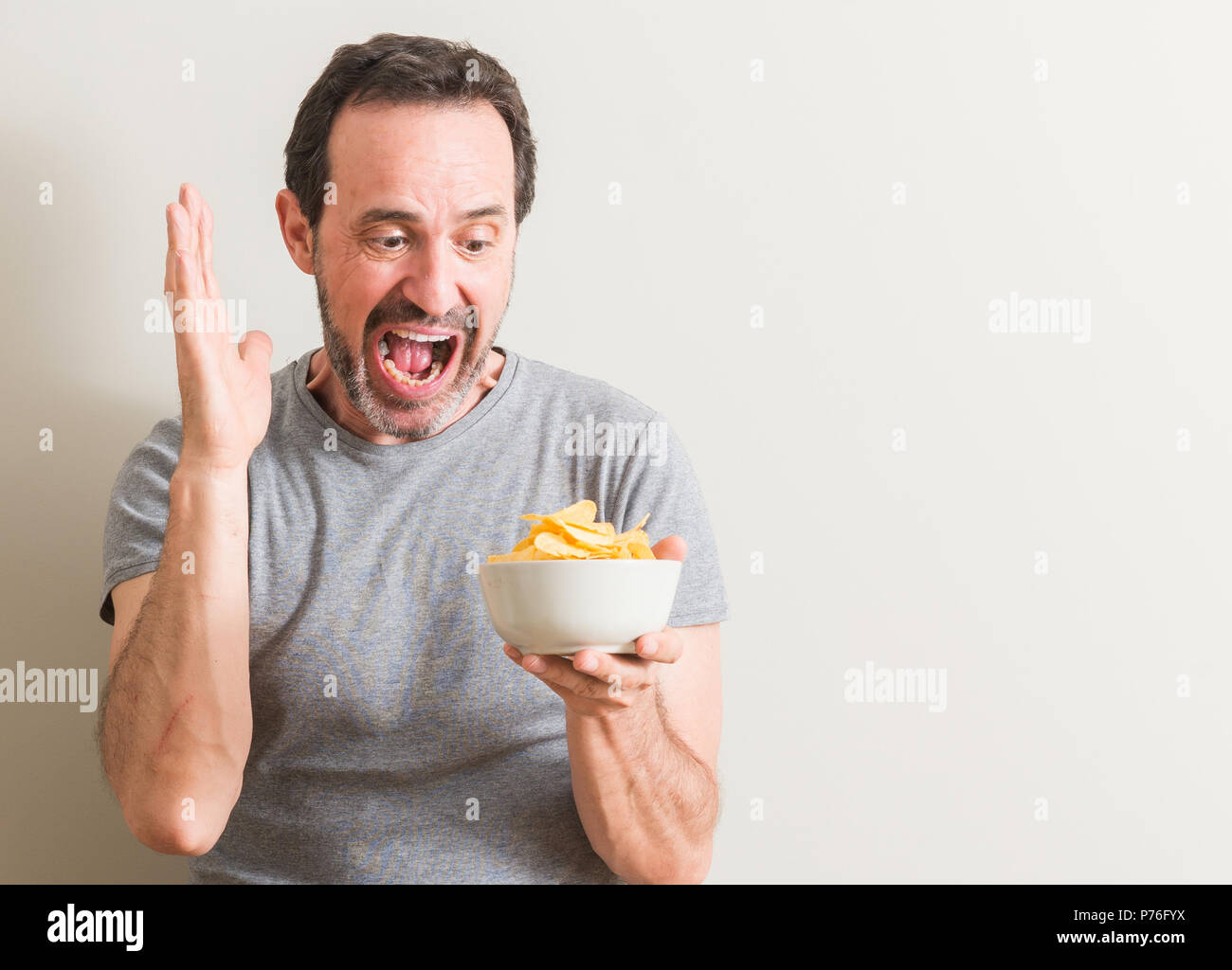 Senior man eating potato chips very happy and excited, winner ...