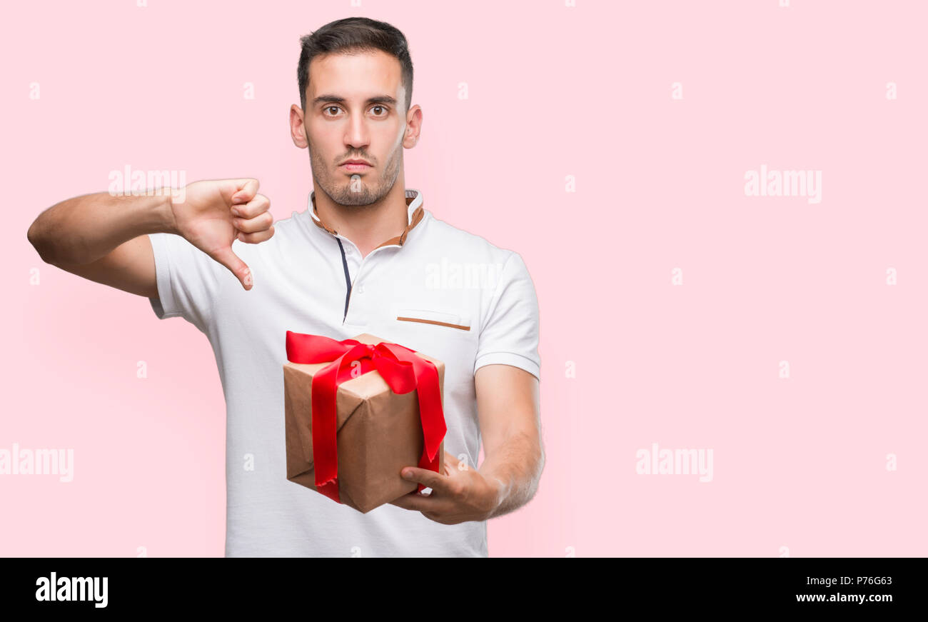 Handsome young man giving a present with angry face, negative sign ...
