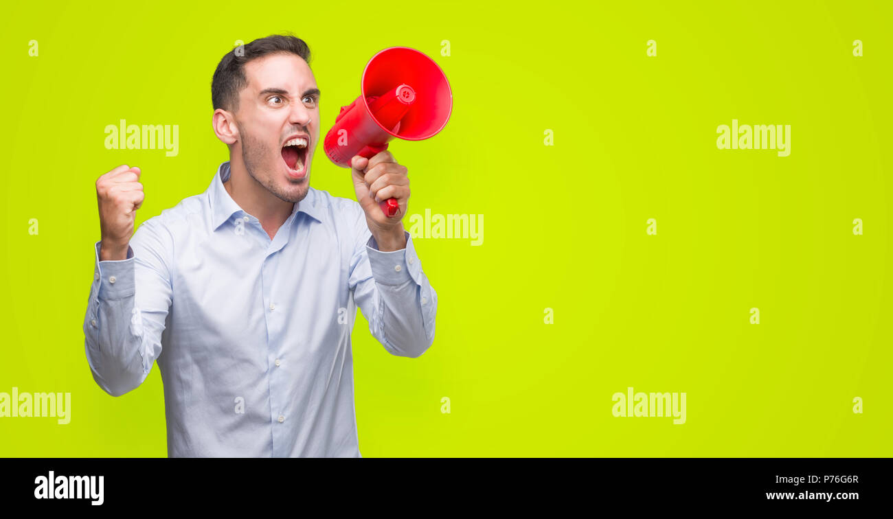 Handsome young man holding microphone annoyed and frustrated shouting ...