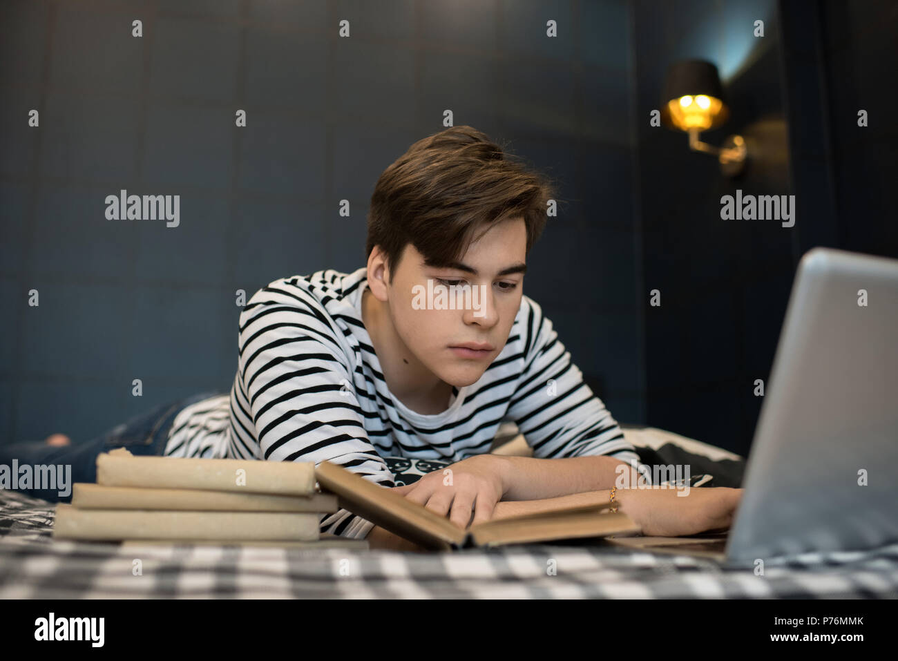 Attractive young male reading pile of books and using laptop computer ...