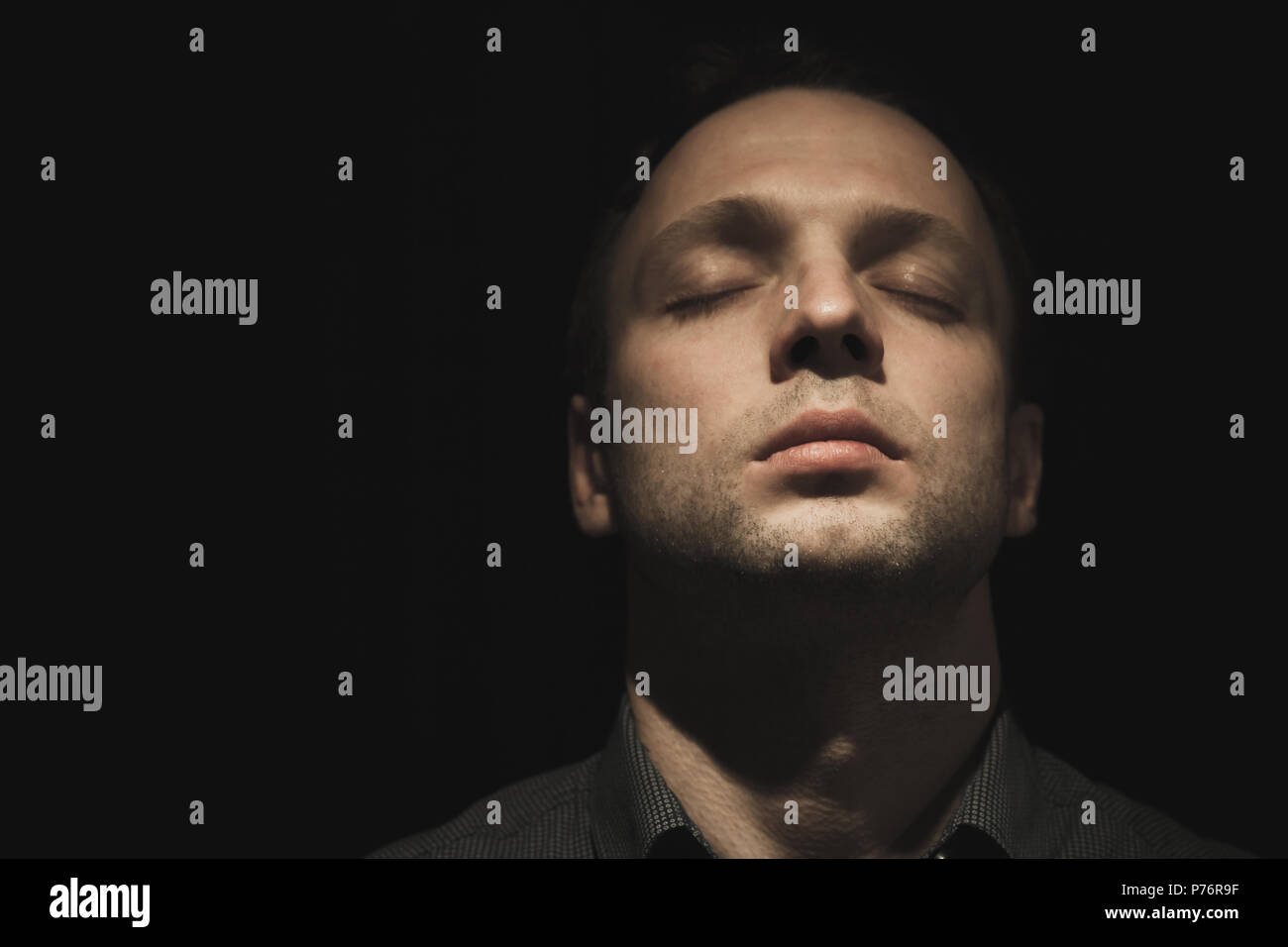 Young European man with closed eyes over black background, low key ...