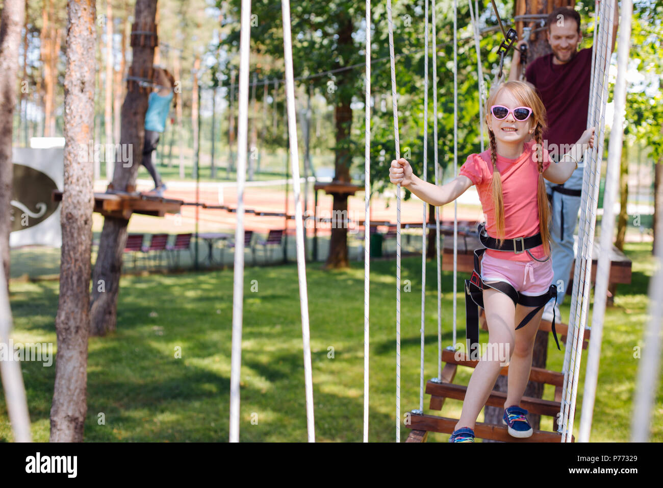 Petite little girl walking along rope bridge at adventure park Stock ...
