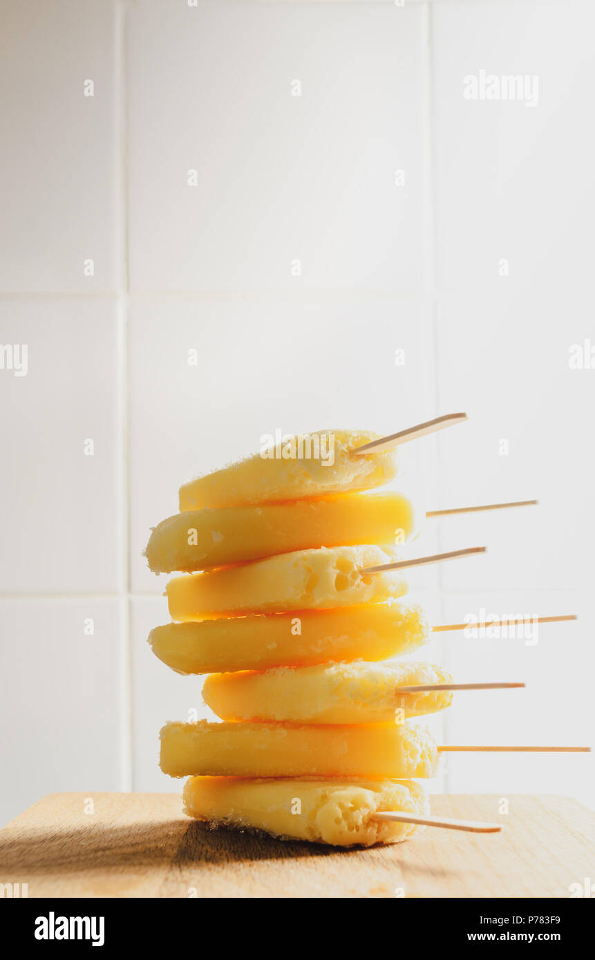 Tall stack of yellow pineapple ice lollies, on a wooden table with ...