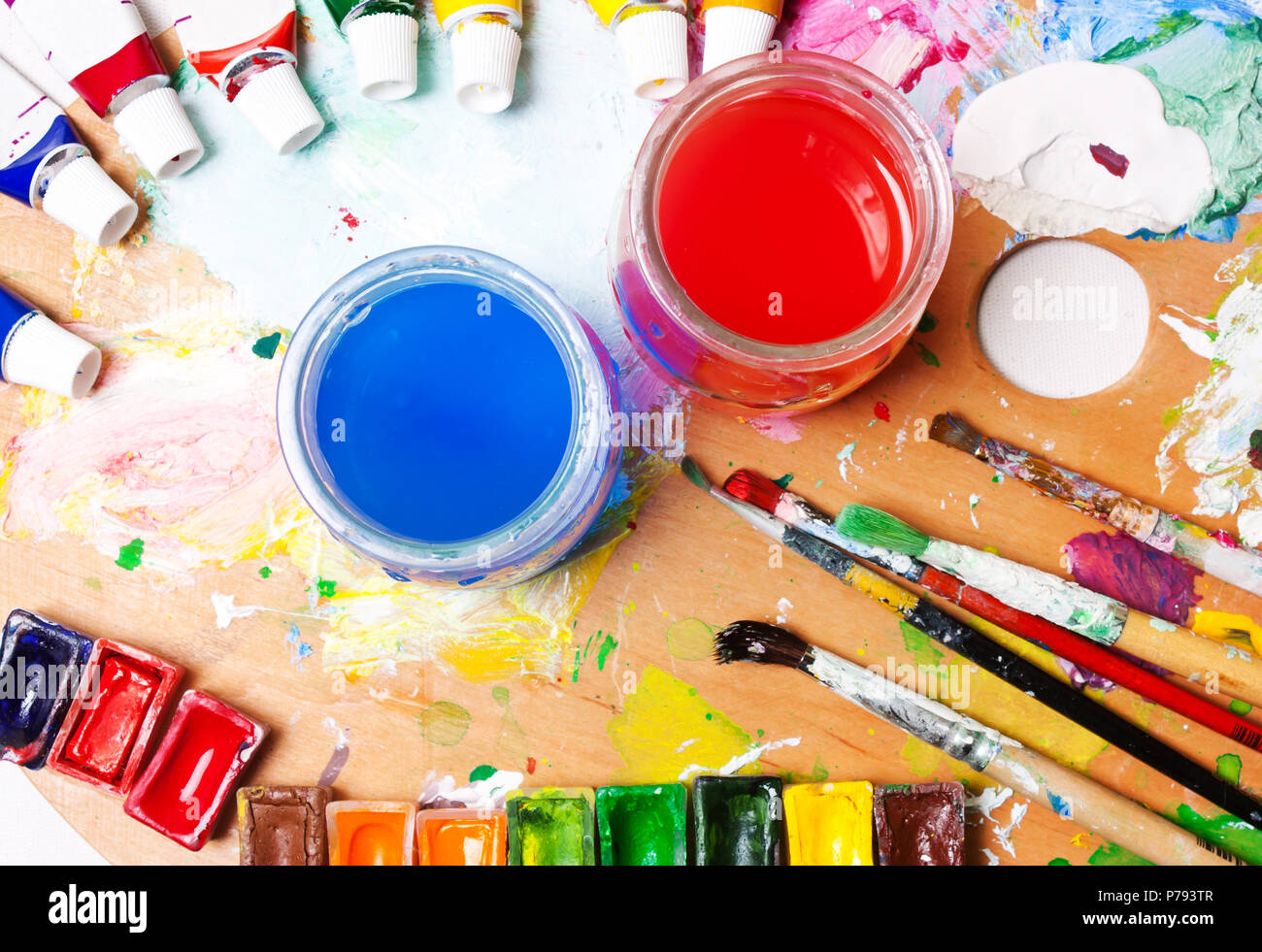 Multicolored paints, brushes, palette, water. Desk, workplace artist ...