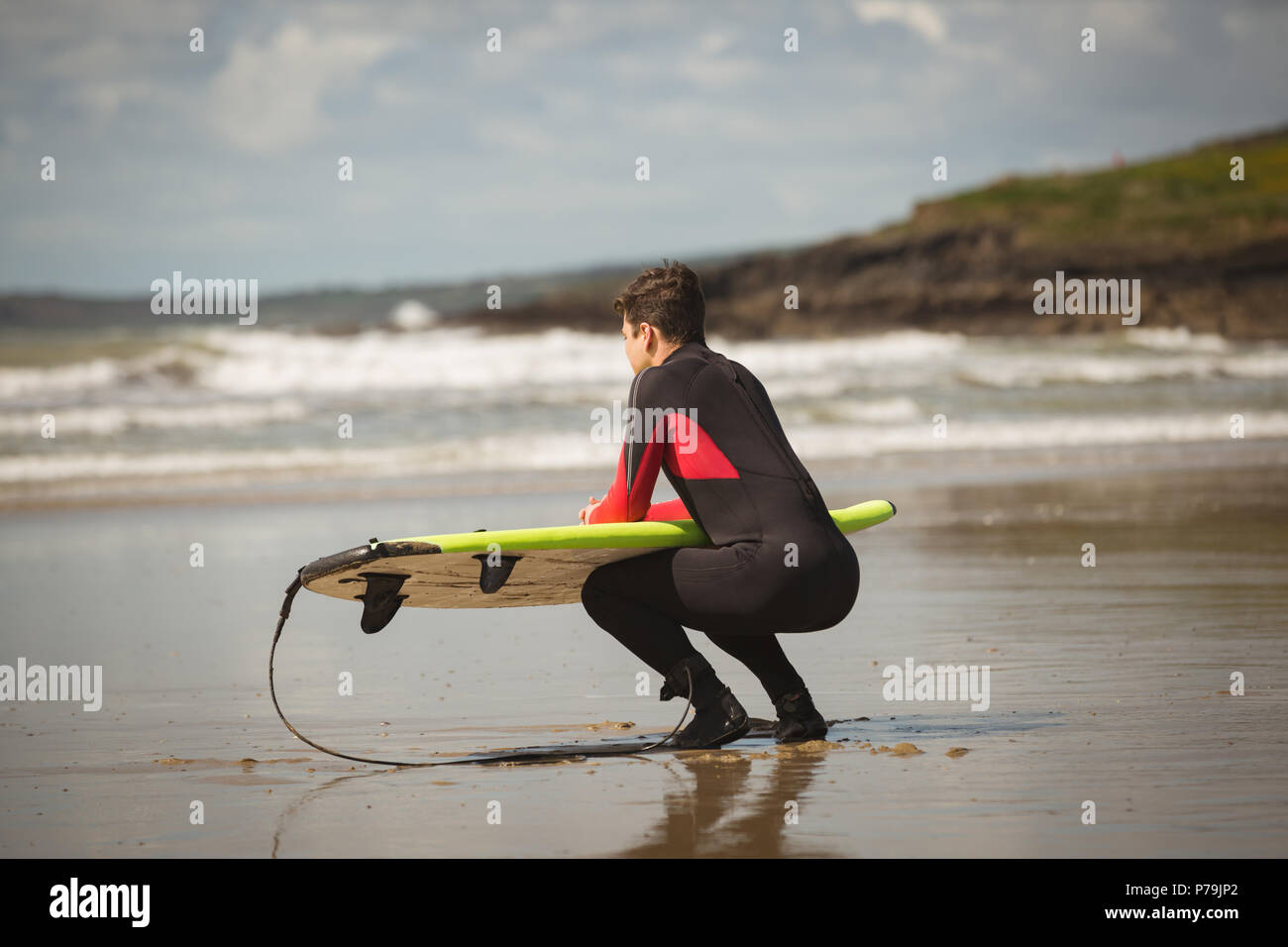 Surfer with surfboard crouching at beach Stock Photo - Alamy