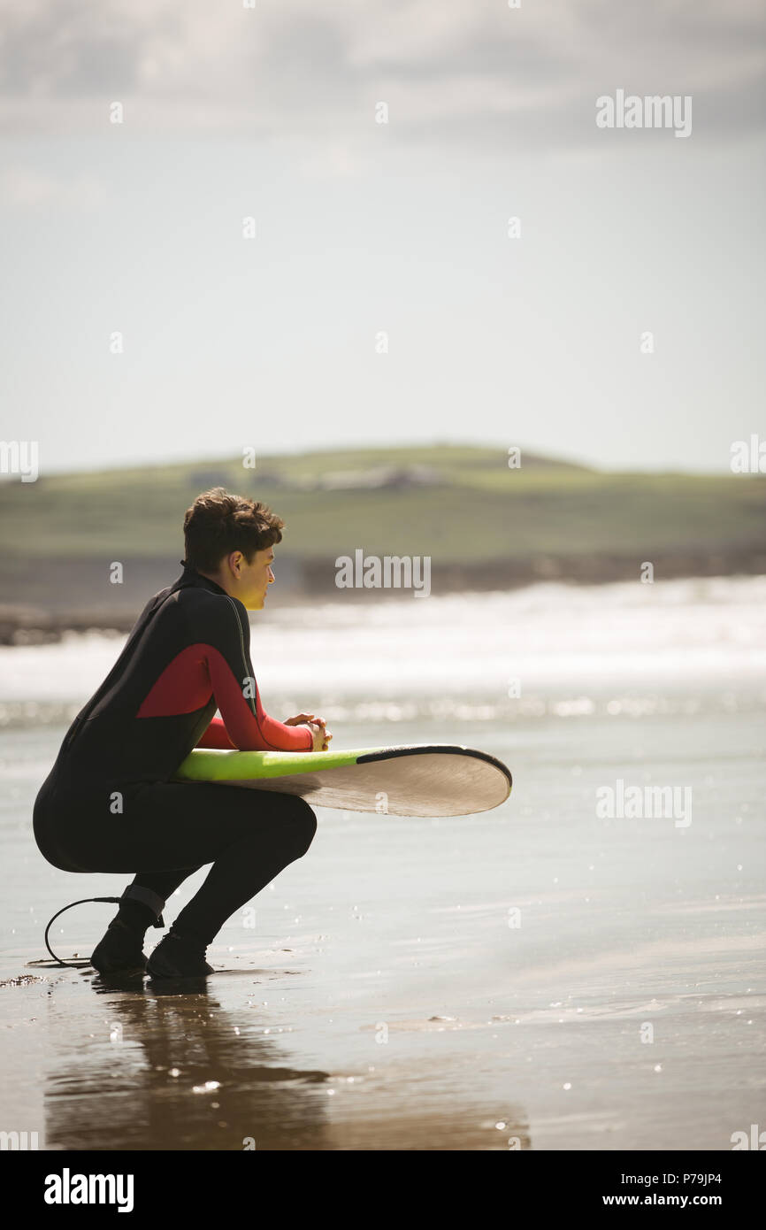 Surfer with surfboard crouching at beach Stock Photo - Alamy