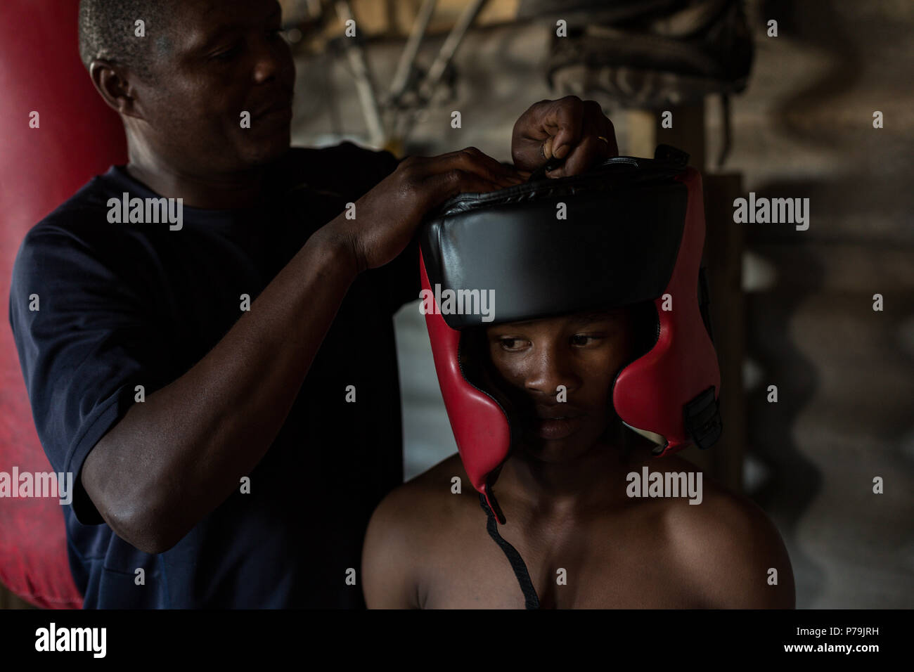 Trainer assisting male boxer to wear headgear Stock Photo - Alamy