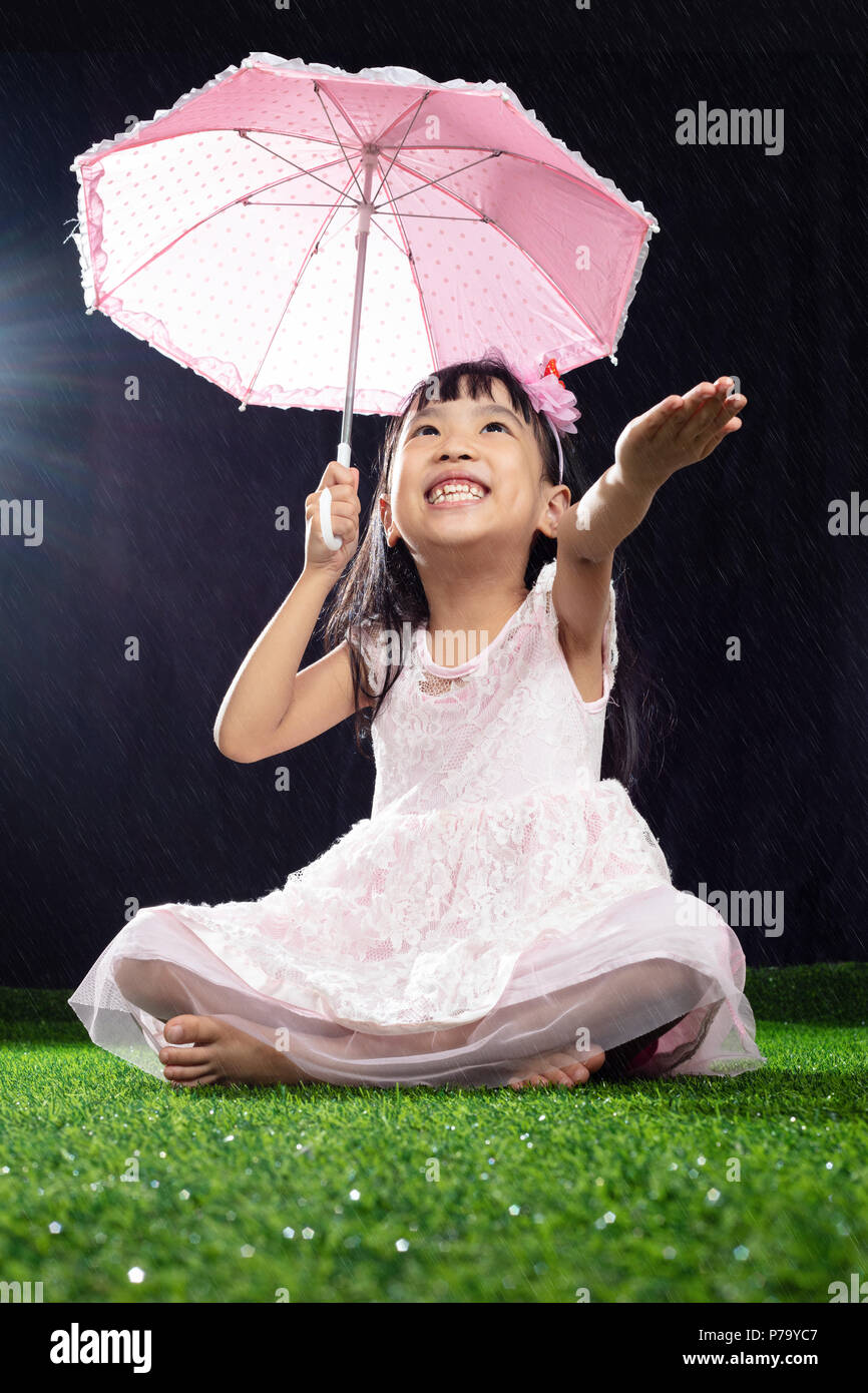 Asian Little Chinese Girl holding umbrella and sitting on the grassland ...