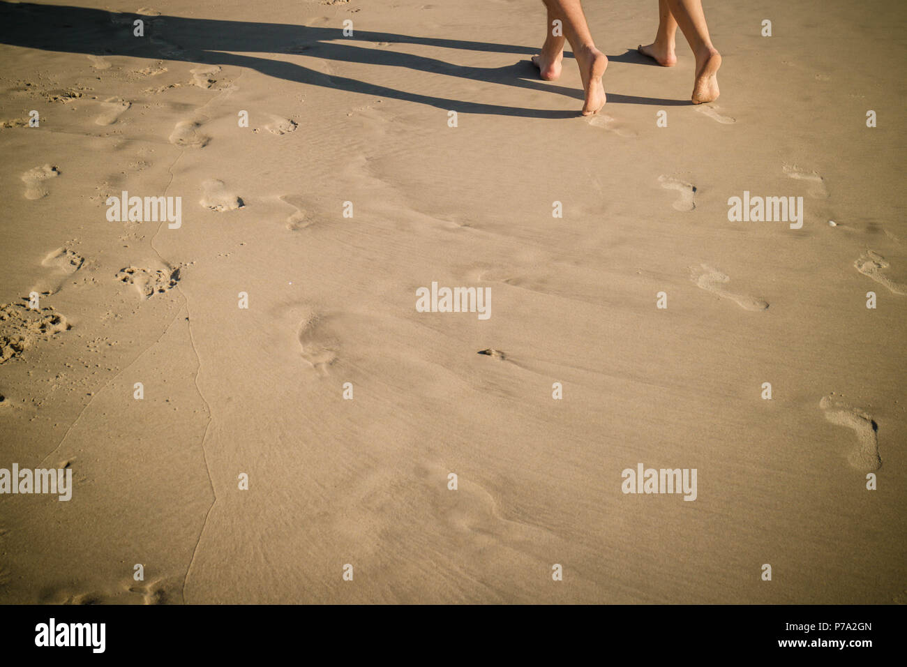 Two pairs of feet walking side by side on the beach with footprints ...