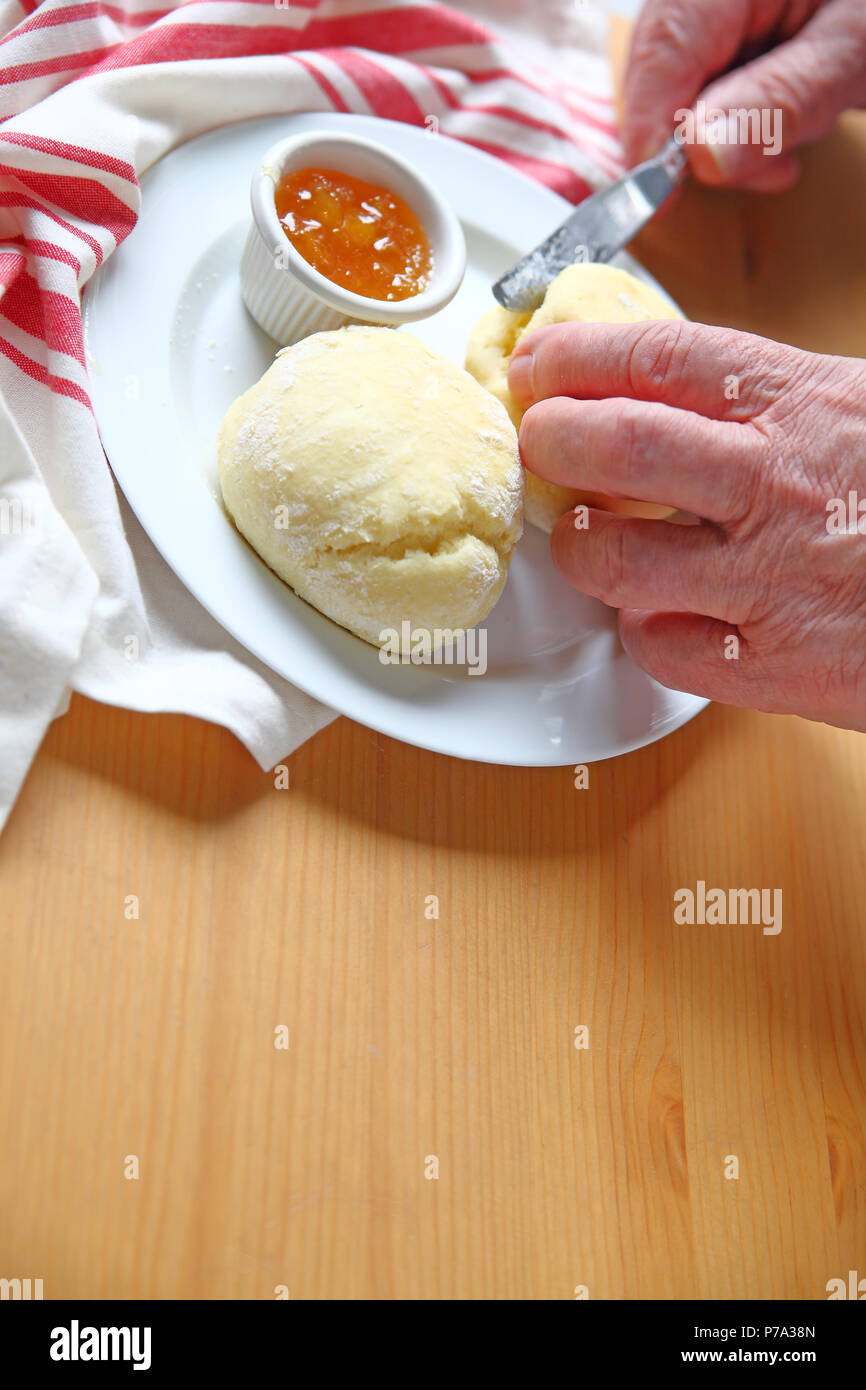Using a dinner knife to break open biscuits with jam alongside Stock ...