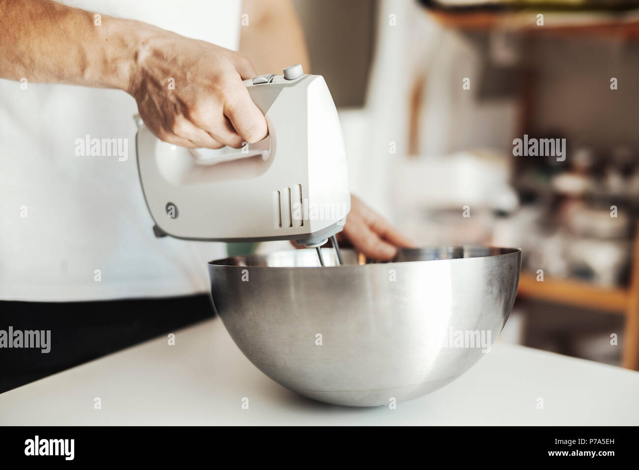 Metal bowl with mixer and hand on white table Stock Photo - Alamy