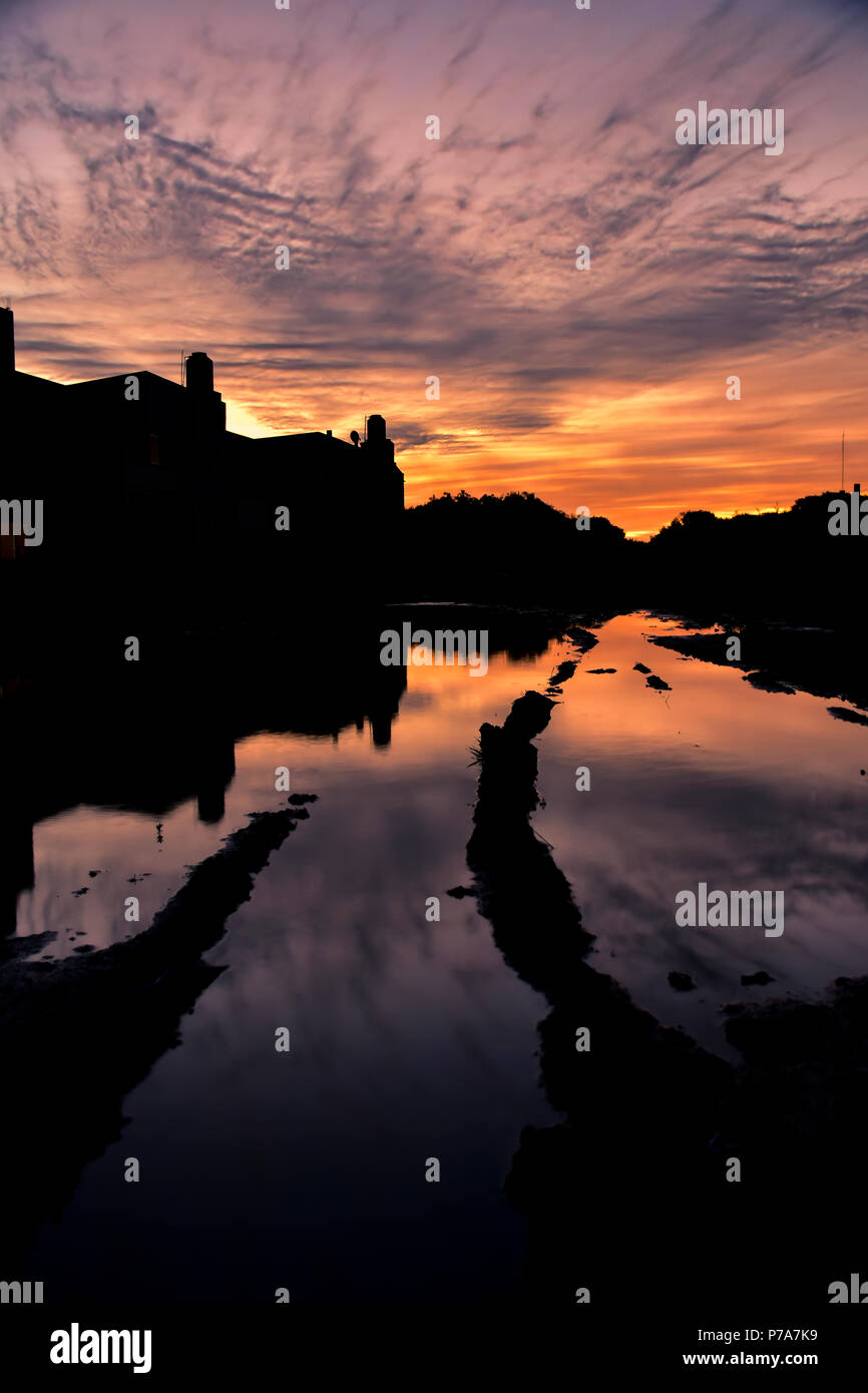 Colourful sunset with reflections of the sky in a puddle after a rainy ...