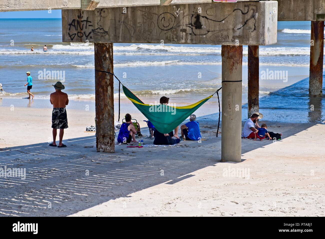 A group of beach goers hang out underneath a concrete pier along the ...