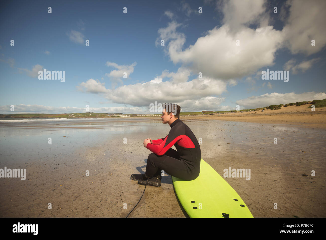 Surfer sitting on the surfboard on beach and looking at sea Stock Photo ...