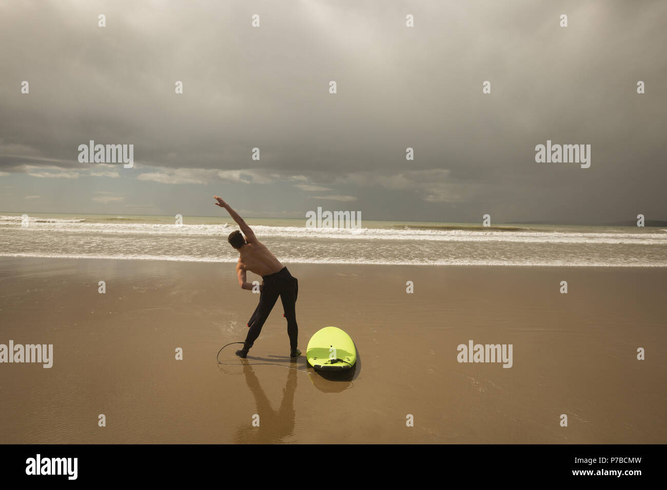 Surfer with surfboard performing stretching exercise at beach Stock ...