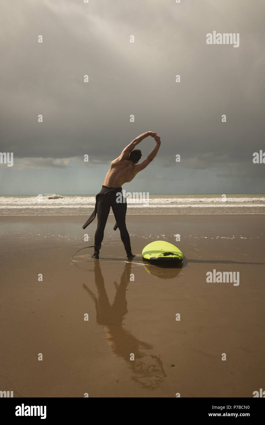 Surfer with surfboard performing stretching exercise at beach Stock ...