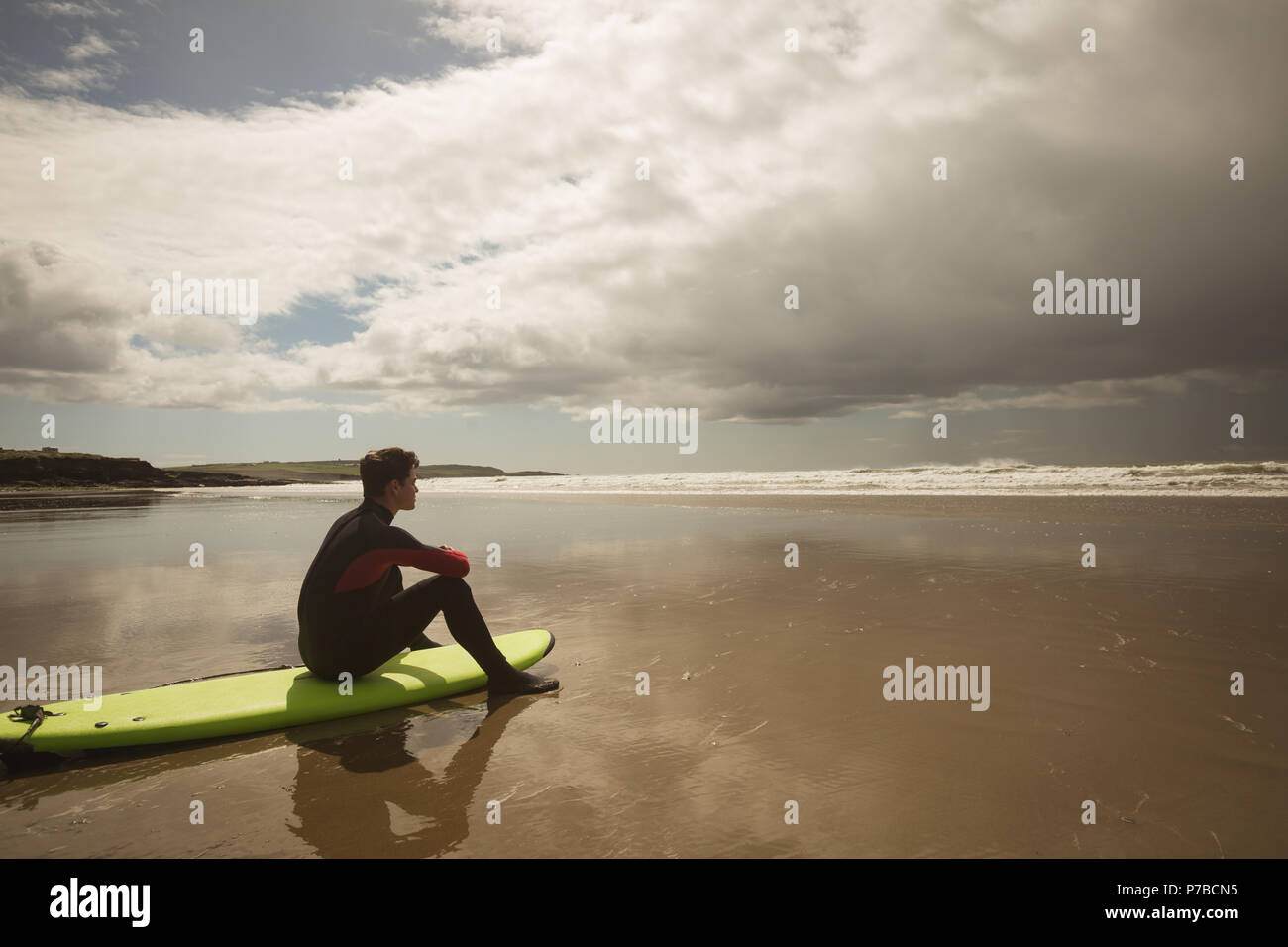 Surfer sitting on the surfboard on beach and looking at sea Stock Photo ...