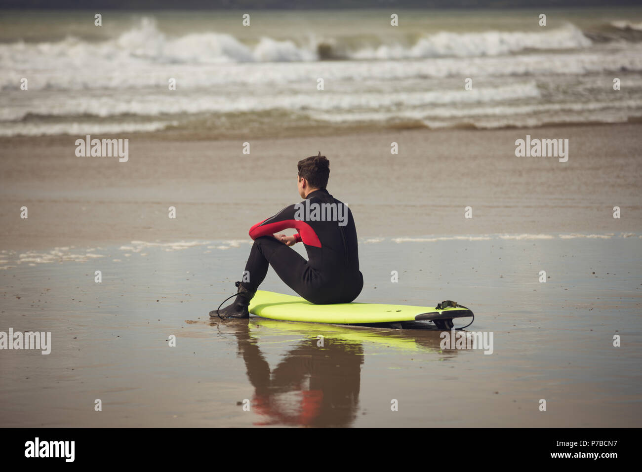 Surfer sitting on the surfboard on beach and looking at sea Stock Photo ...