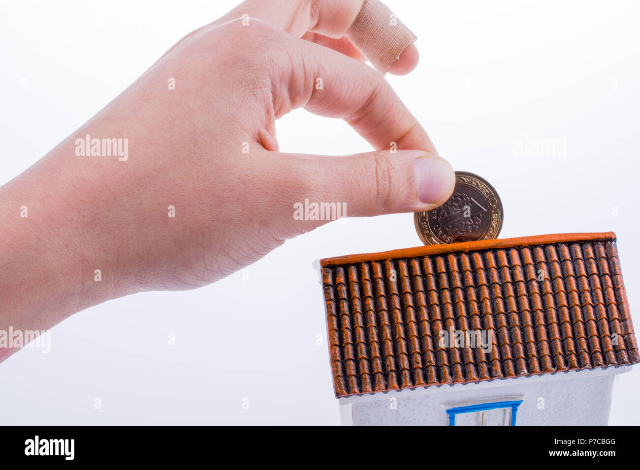 Hand dropping coin into the moneybox in the shape of a model house ...