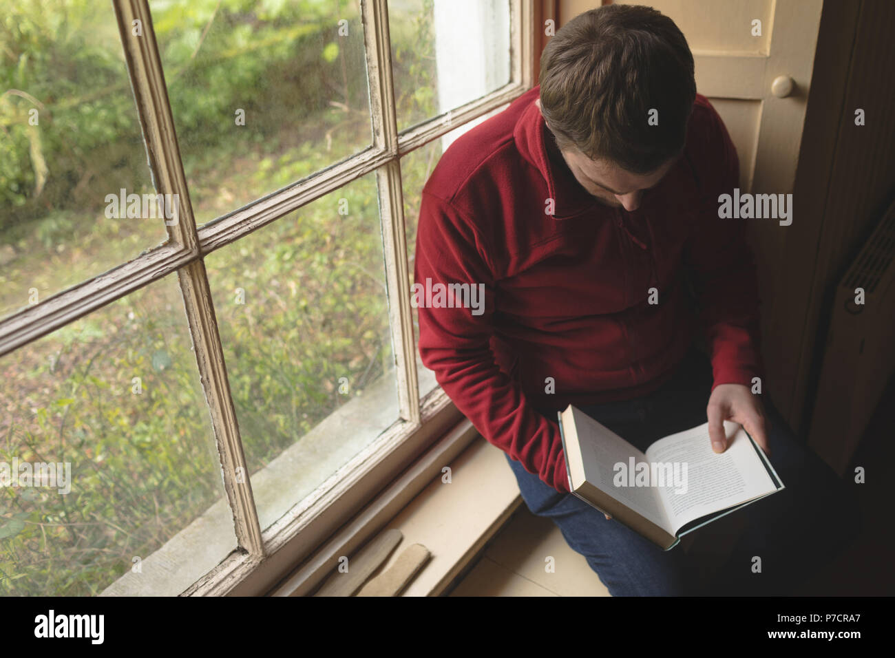 Man reading a book near window Stock Photo - Alamy