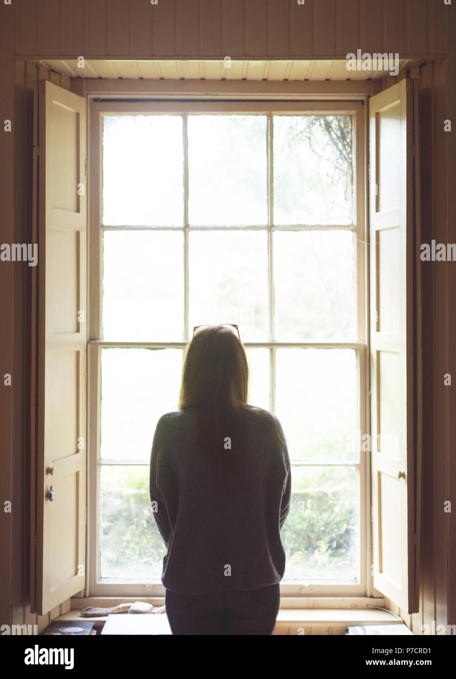 Woman looking through window at home Stock Photo - Alamy