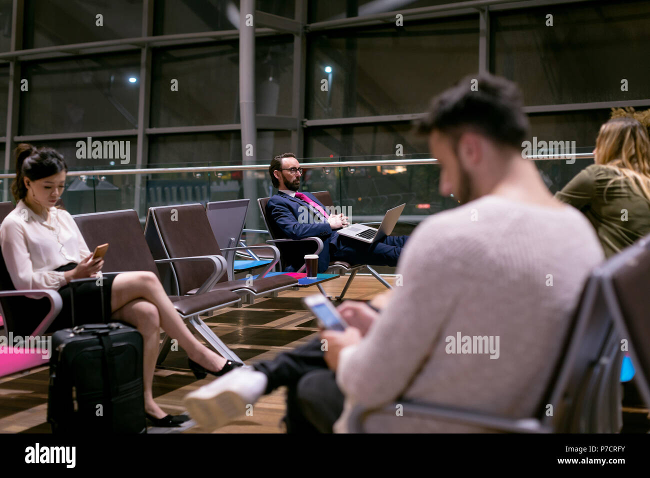 Commuters using electronic devices in waiting room Stock Photo - Alamy