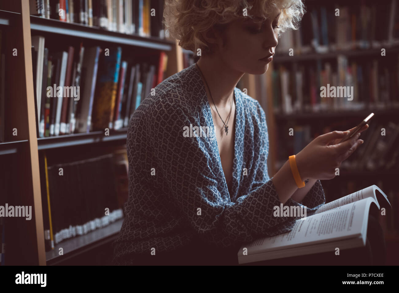Woman using mobile phone while reading a book Stock Photo - Alamy