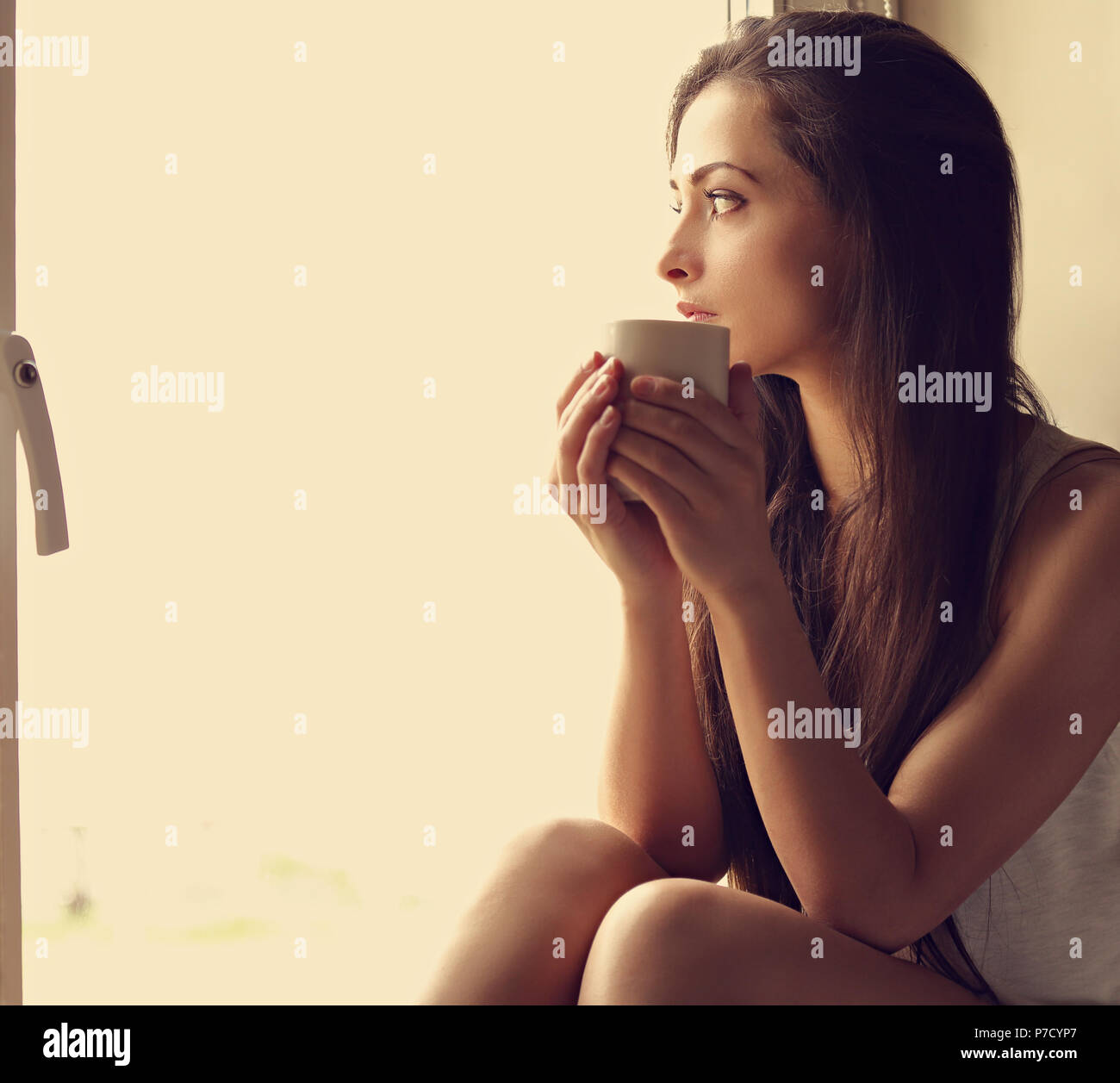 Beautiful lonely woman sitting near the window and looking sad holding ...