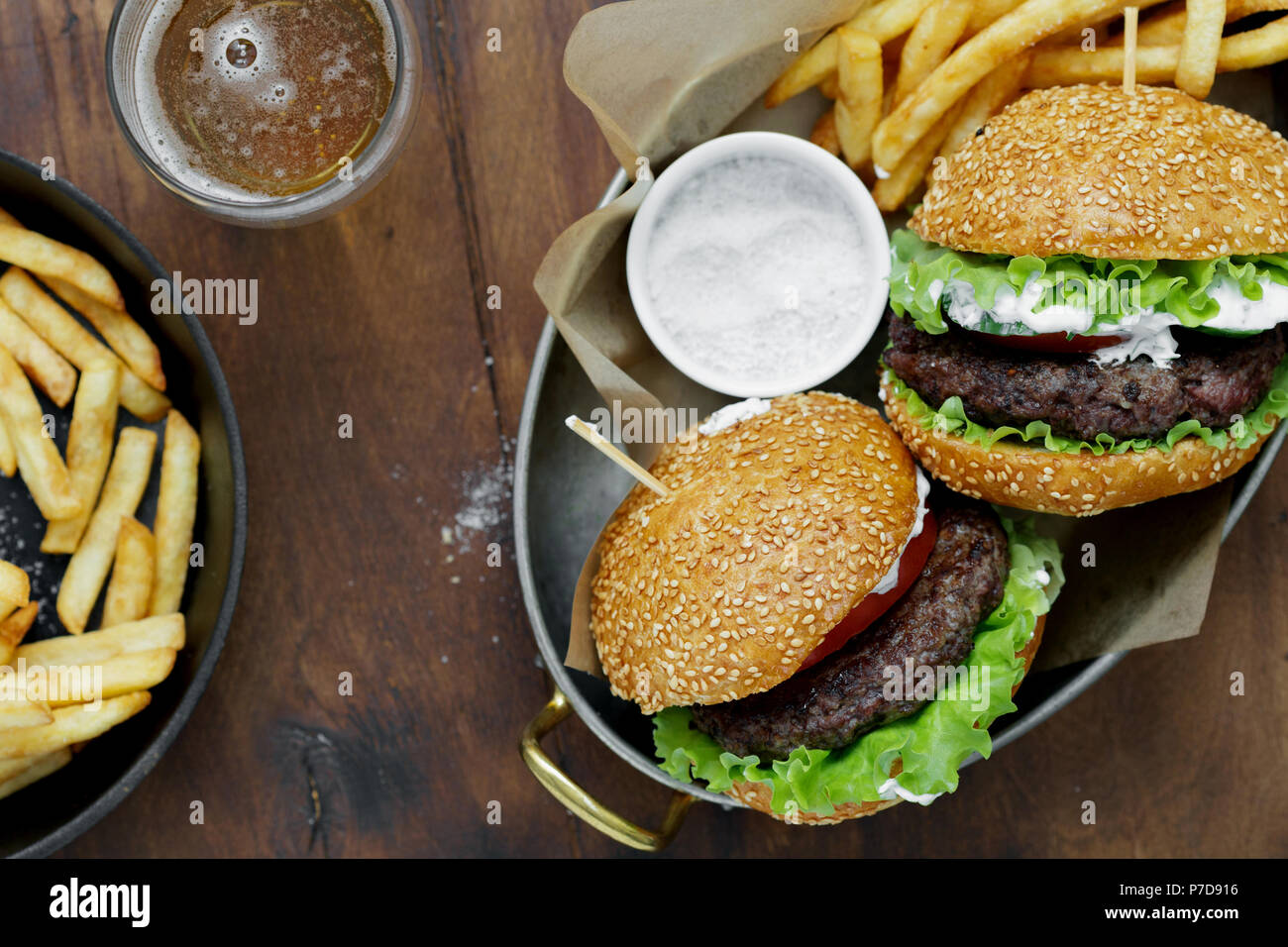 Top view burgers, french fries, sauce served in frying pans on wooden ...