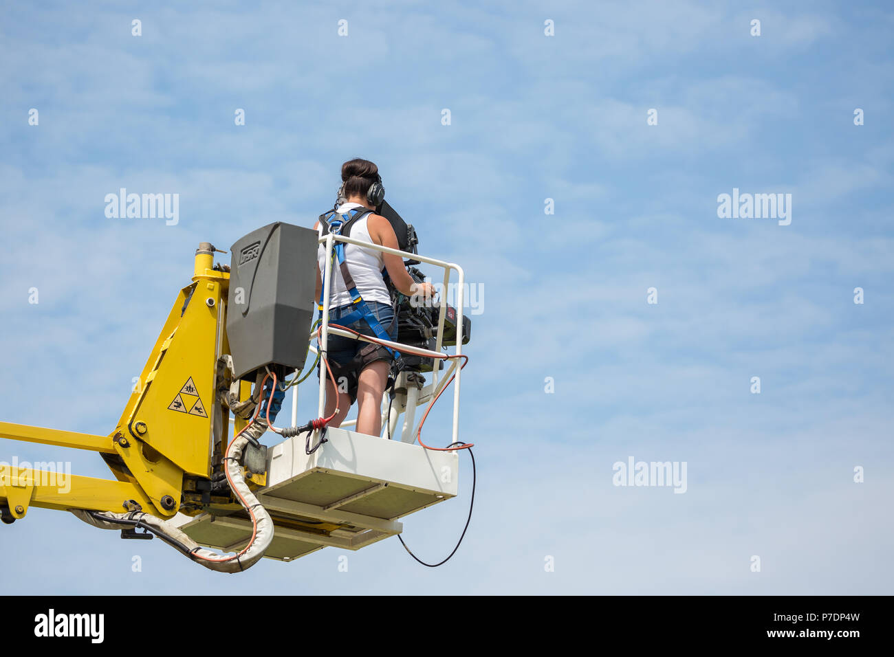 Rear view of single television camerawoman on elevated platform raised ...