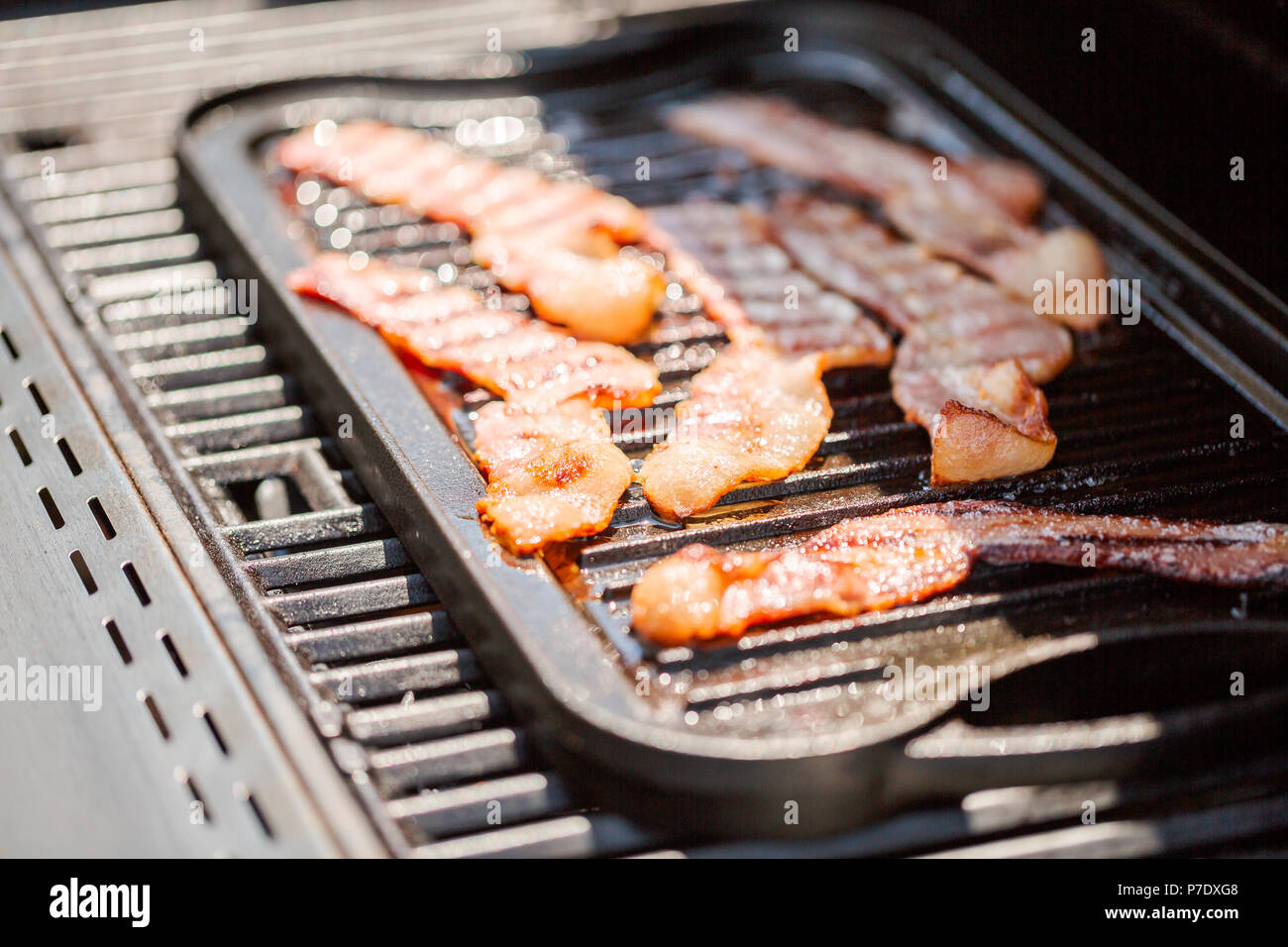 Grilling bacon strips on cast iron griddle in outdoor gas grill Stock ...