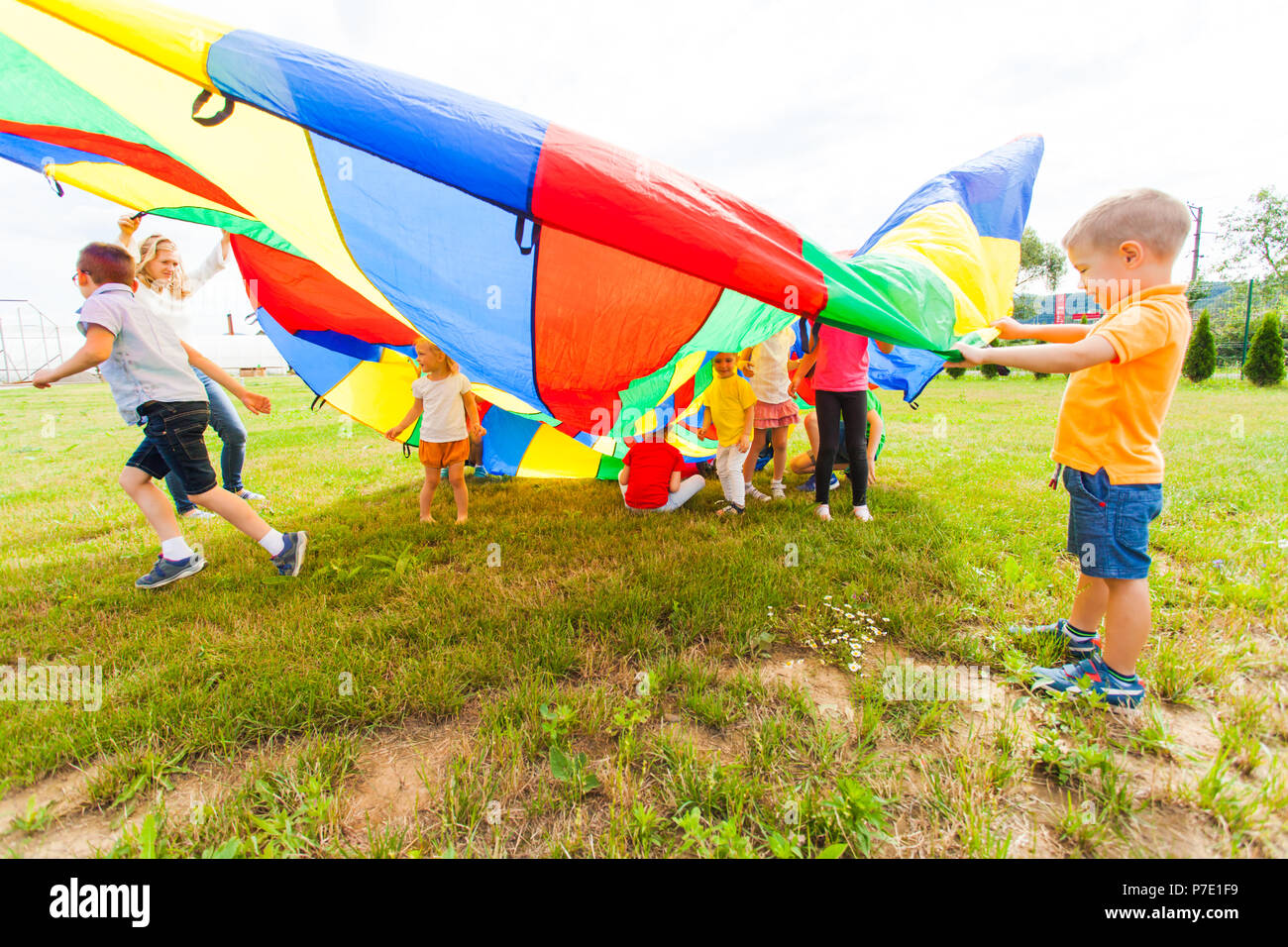 Small boy is covering kids with colorful parachute Stock Photo - Alamy
