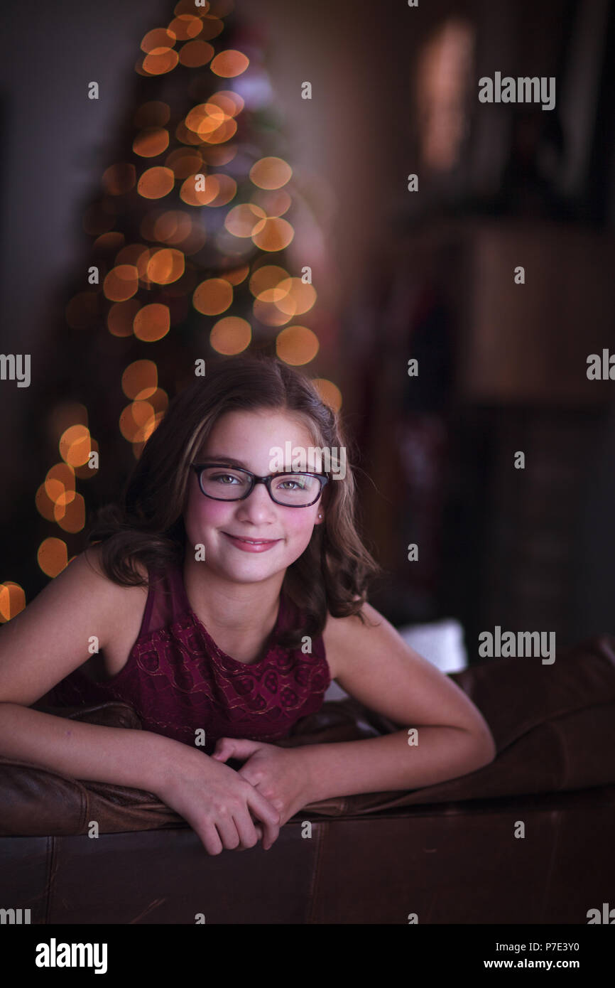Girl leaning over sofa, smiling, Christmas tree in background Stock ...