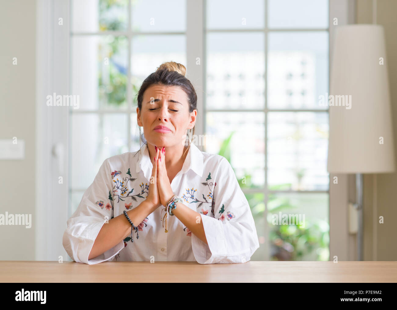 Young woman at home begging and praying with hands together with hope ...