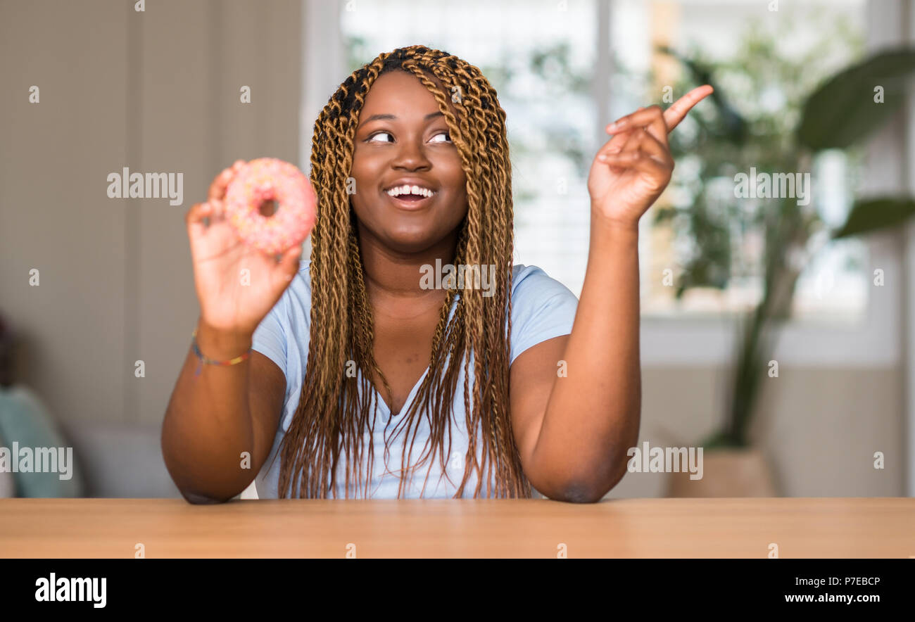 African american woman eating doughnut very happy pointing with hand ...