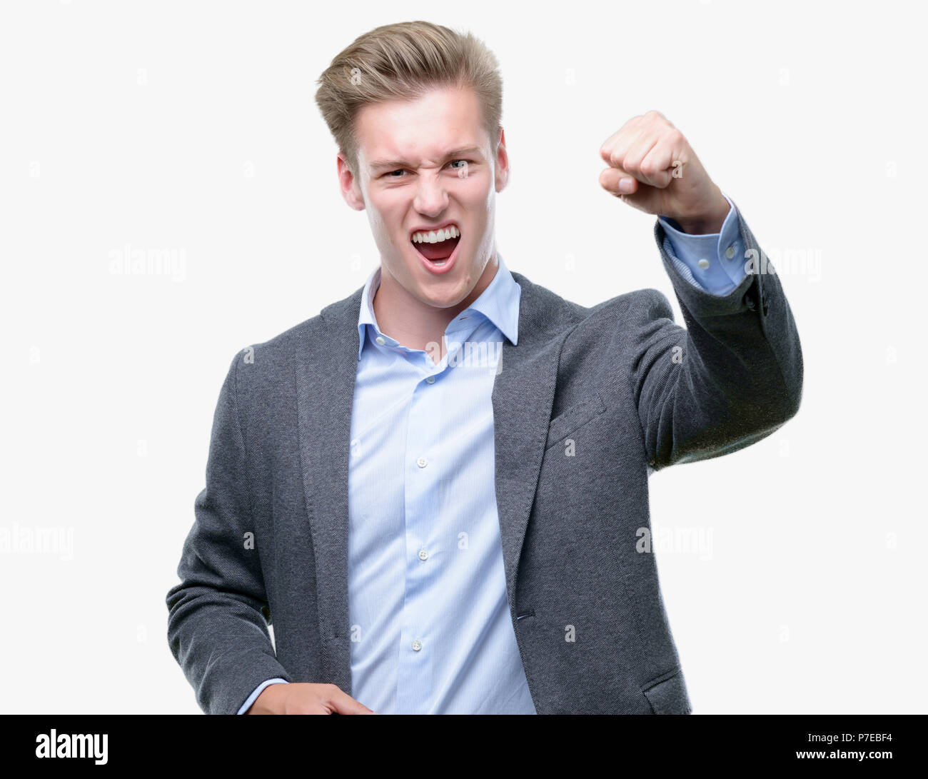 Young handsome blond business man angry and mad raising fist frustrated ...