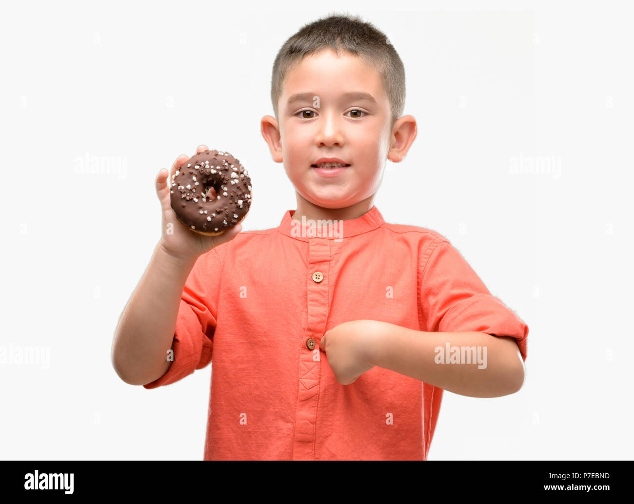 Dark haired little child eating doughnut with surprise face pointing ...