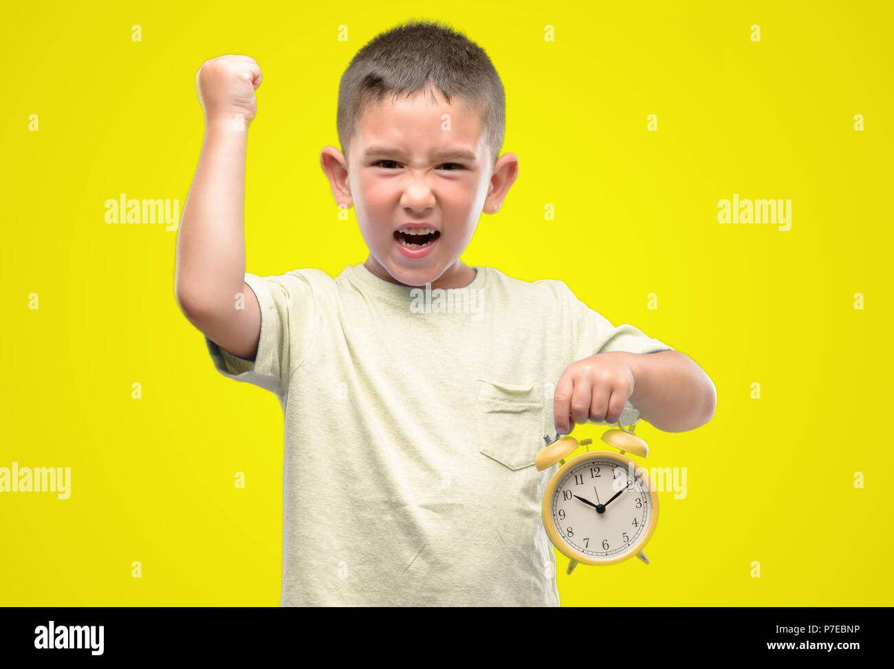 Little child holding alarm clock annoyed and frustrated shouting with ...