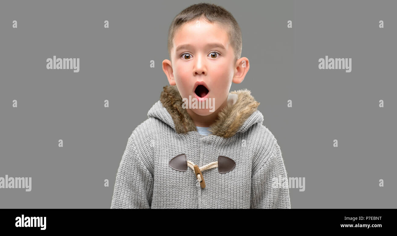 Dark haired little child wearing a coat scared in shock with a surprise ...