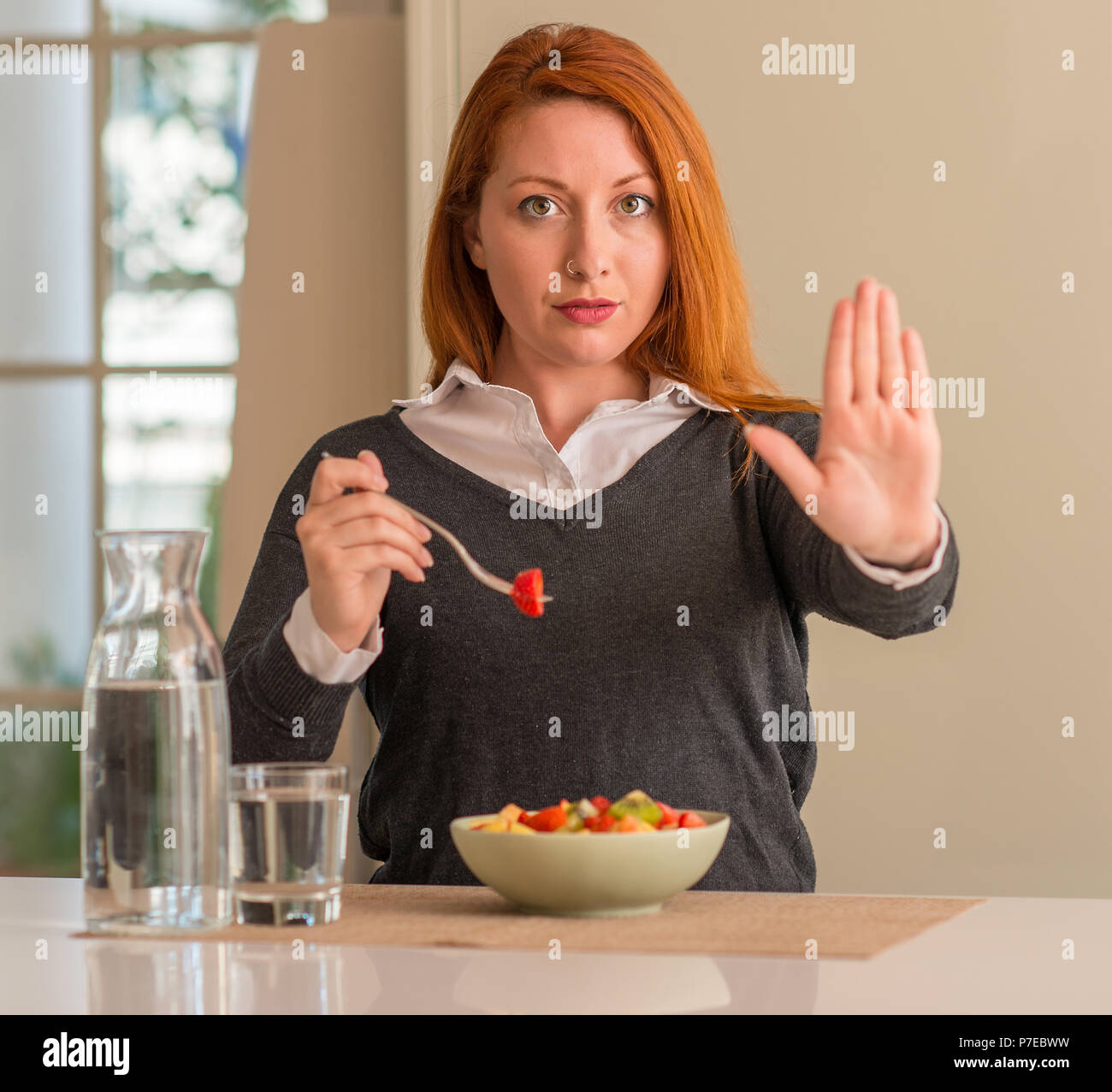 Redhead woman eating fruit bowl, kiwi and strawberry at home with open ...