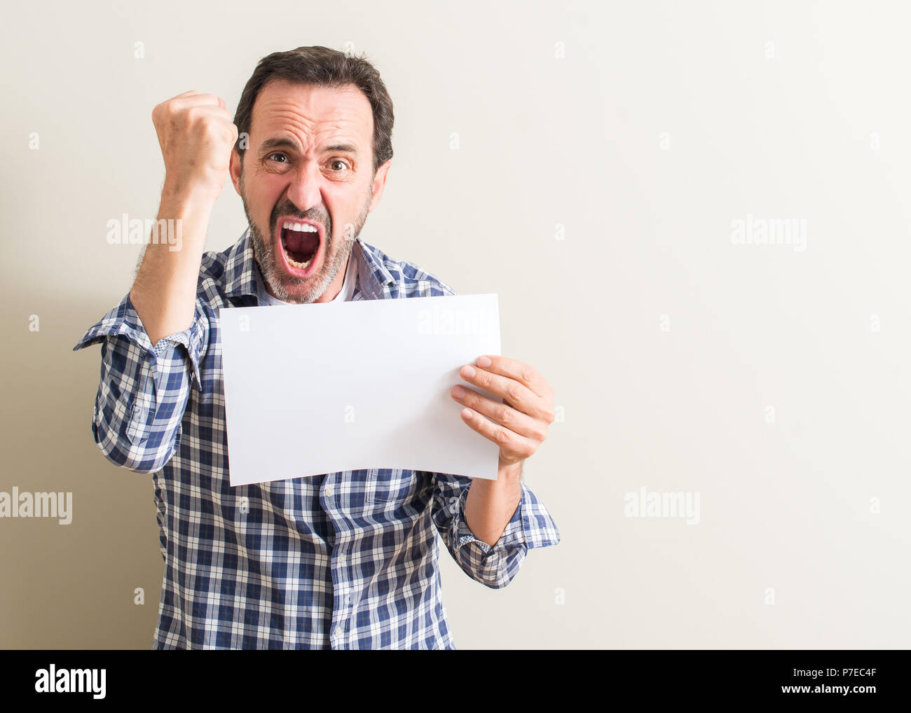 Senior man holding blank paper sheet annoyed and frustrated shouting ...