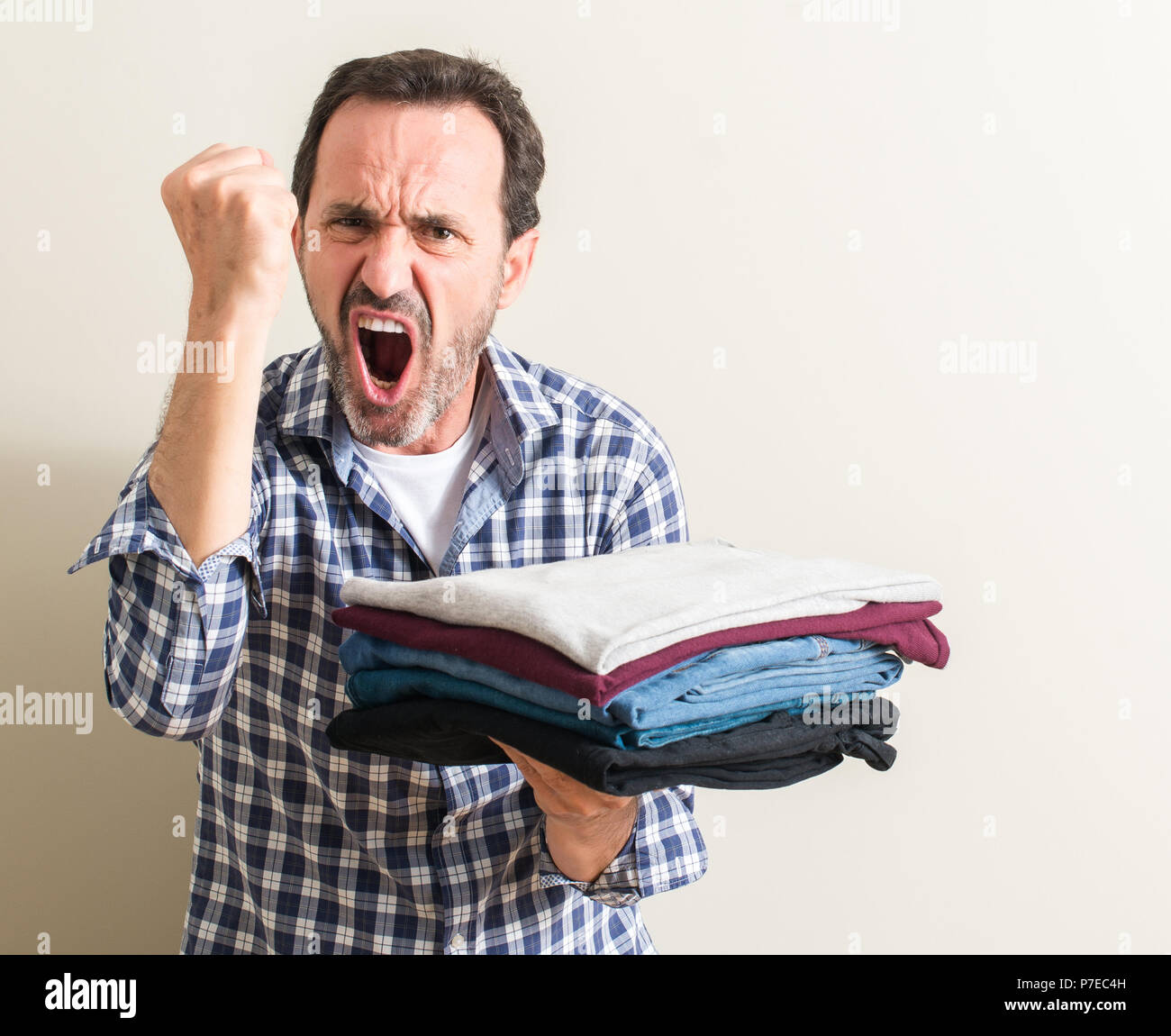 Senior man holding folded laundry clothes annoyed and frustrated ...