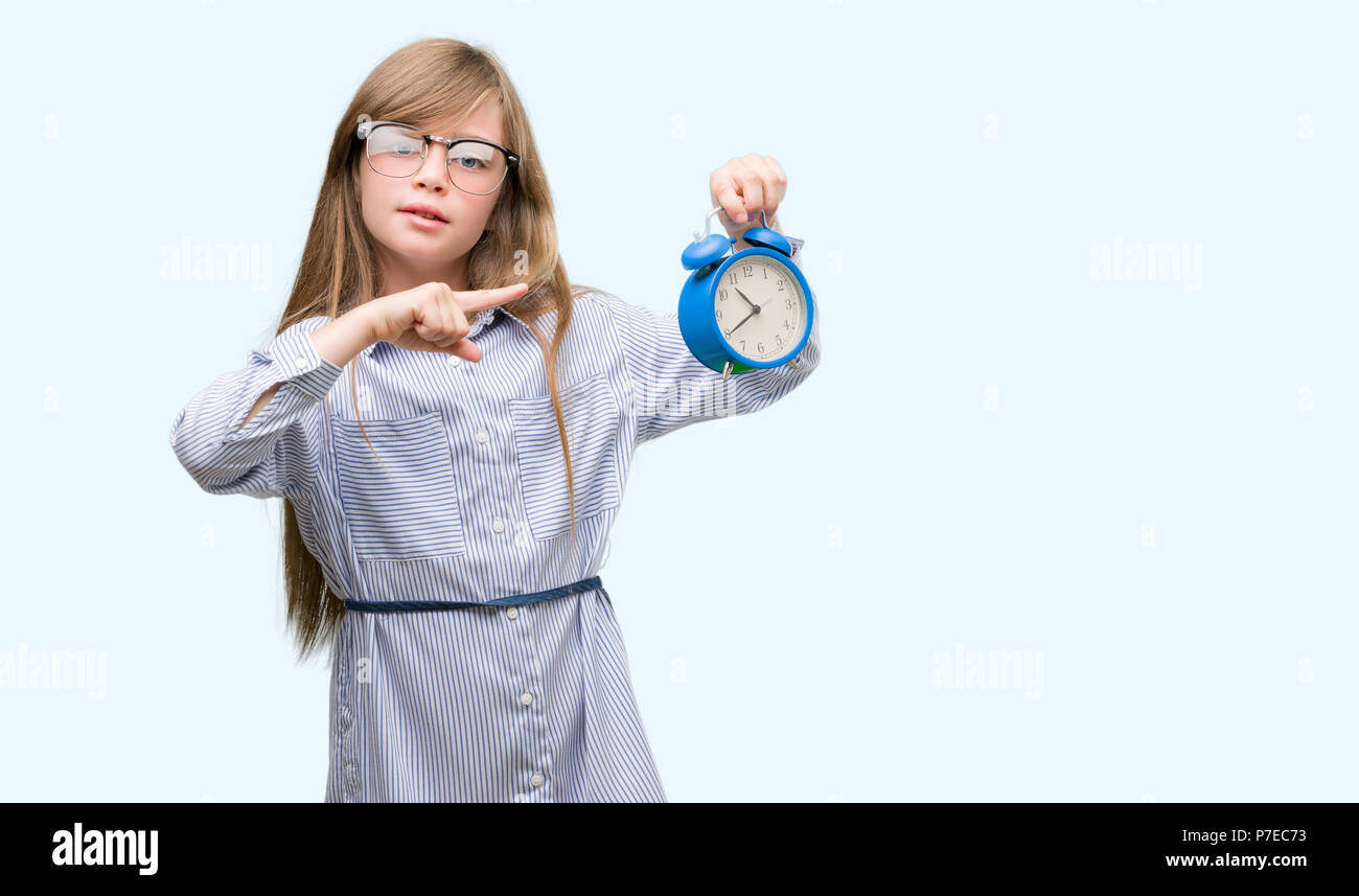 Young blonde child holding alarm clock very happy pointing with hand ...