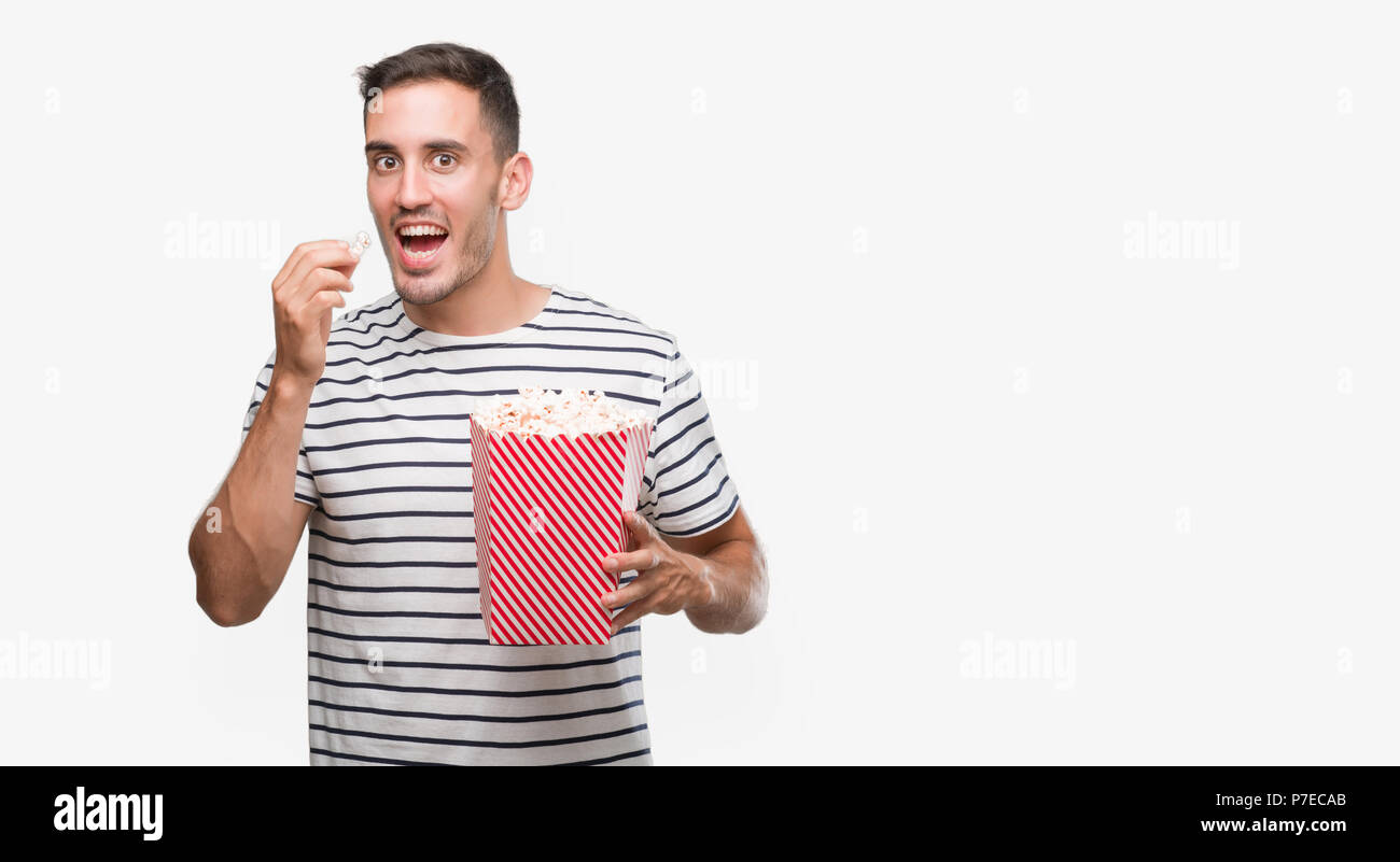 Handsome young man eating popcorn with a happy face standing and ...