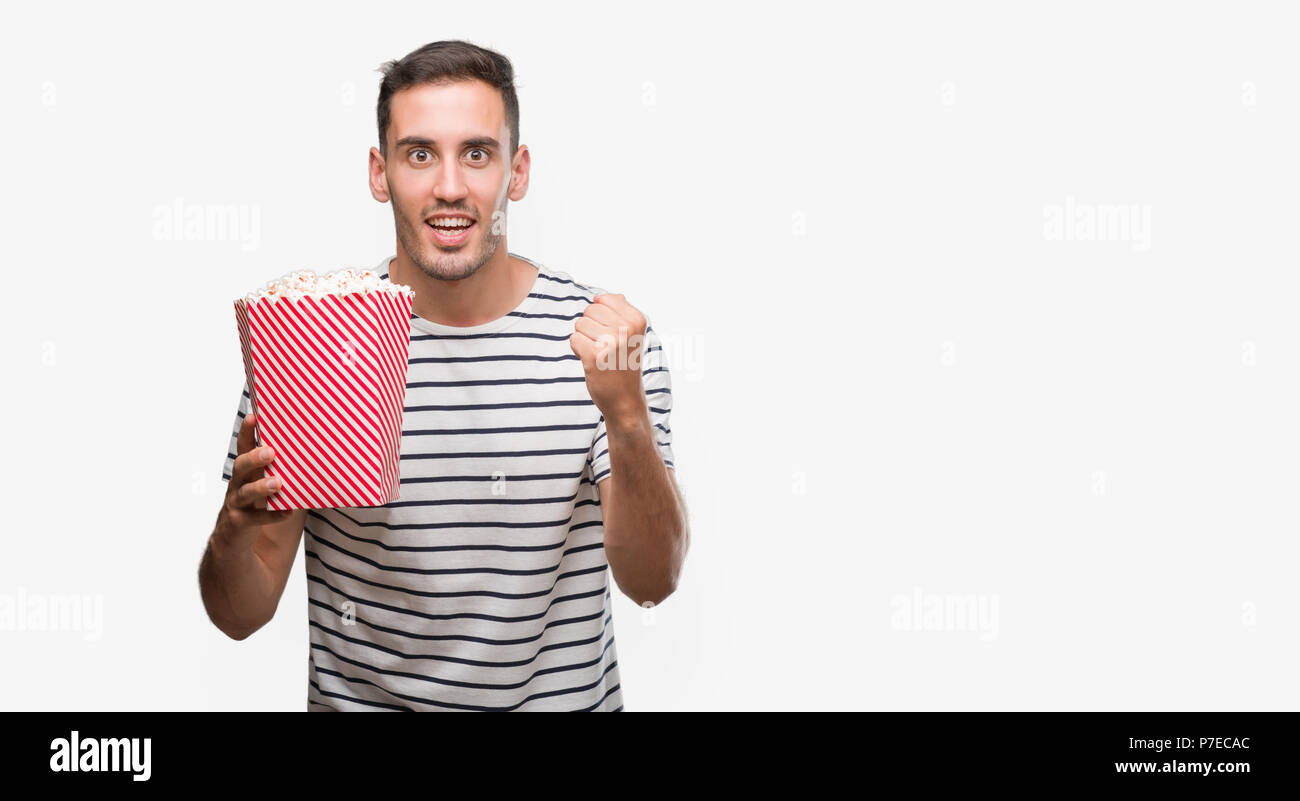 Handsome young man eating popcorn screaming proud and celebrating ...