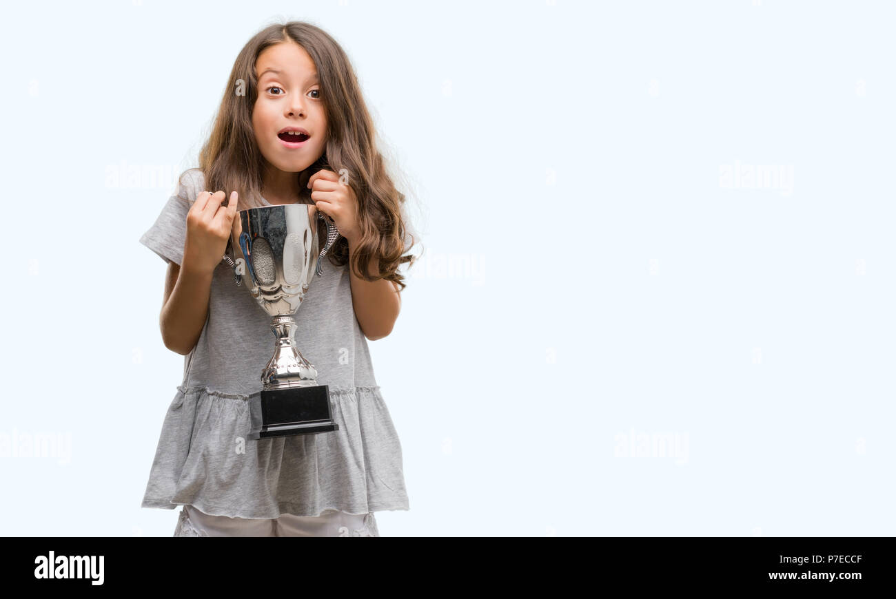 Brunette hispanic girl holding a trophy scared in shock with a surprise ...