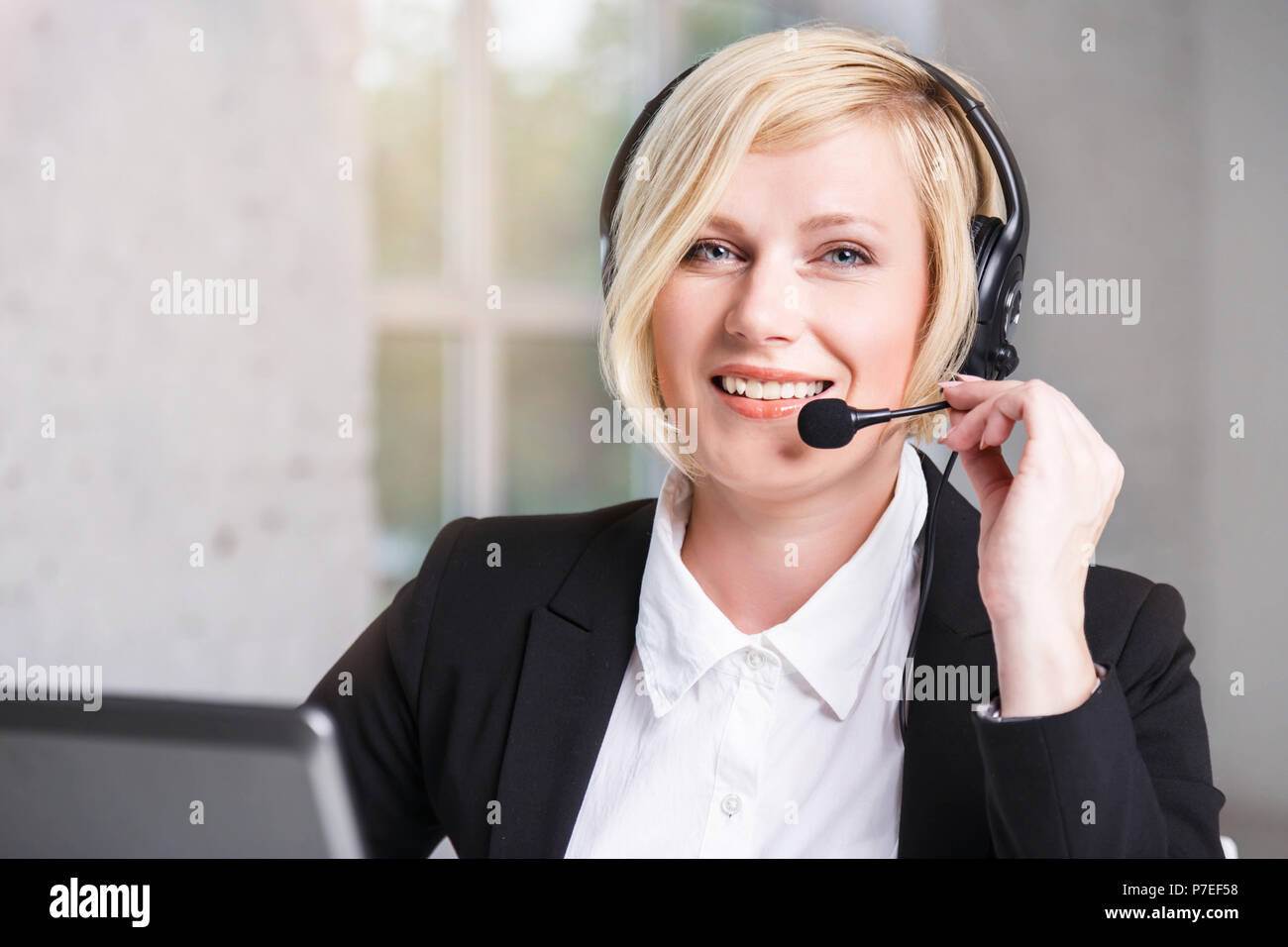 Portrait of beautiful smiling blonde woman, call center operator dressed in black stylish suit ...